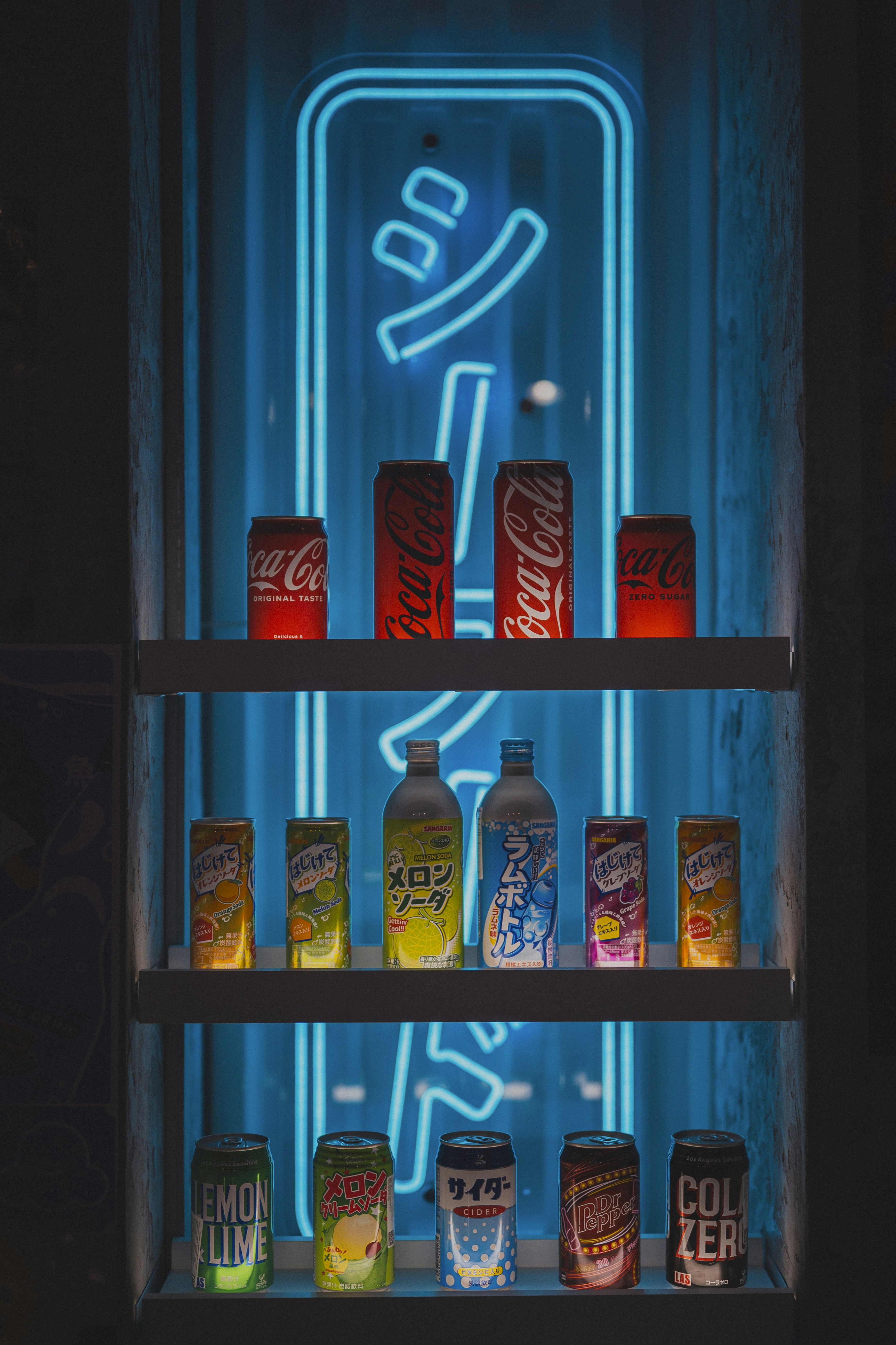 Blue Neon Backdrop Illuminates a Three-Tier Coca-Cola Shelf of Cans and Colorful Bottles