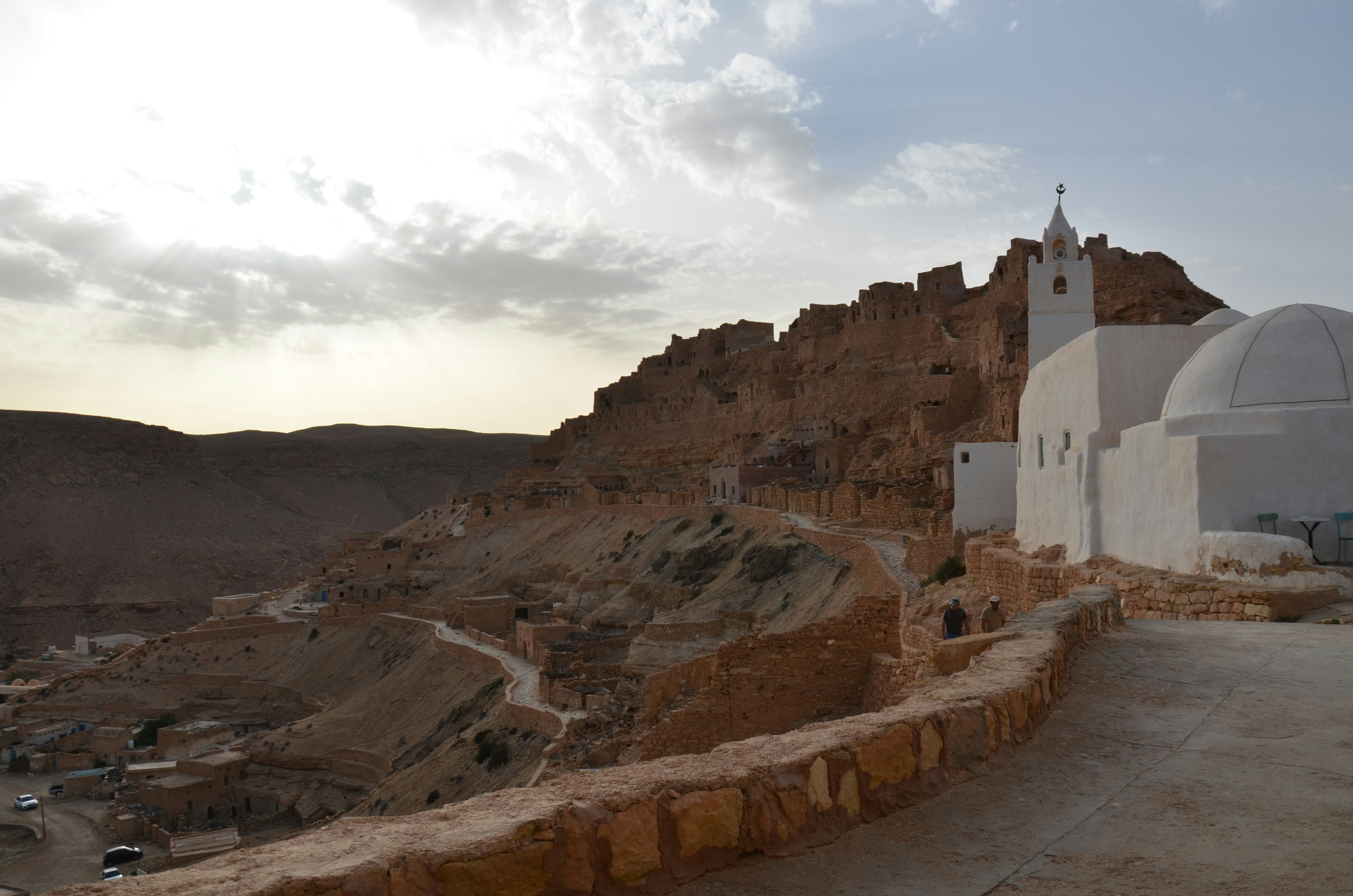 Historic cliffside village with whitewashed buildings and ruins under a dramatic sky.