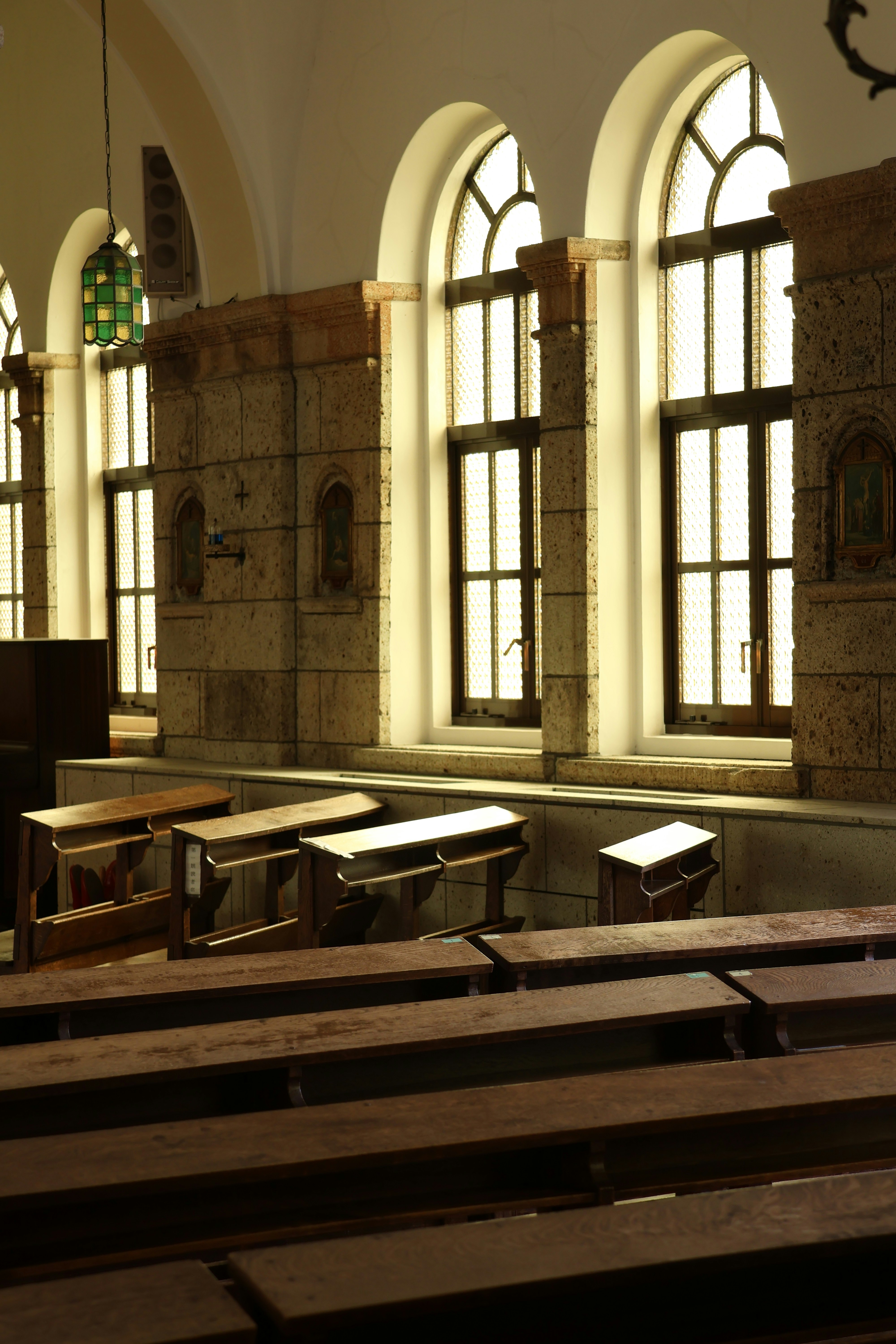 Rows of wooden benches inside a church with arched windows.