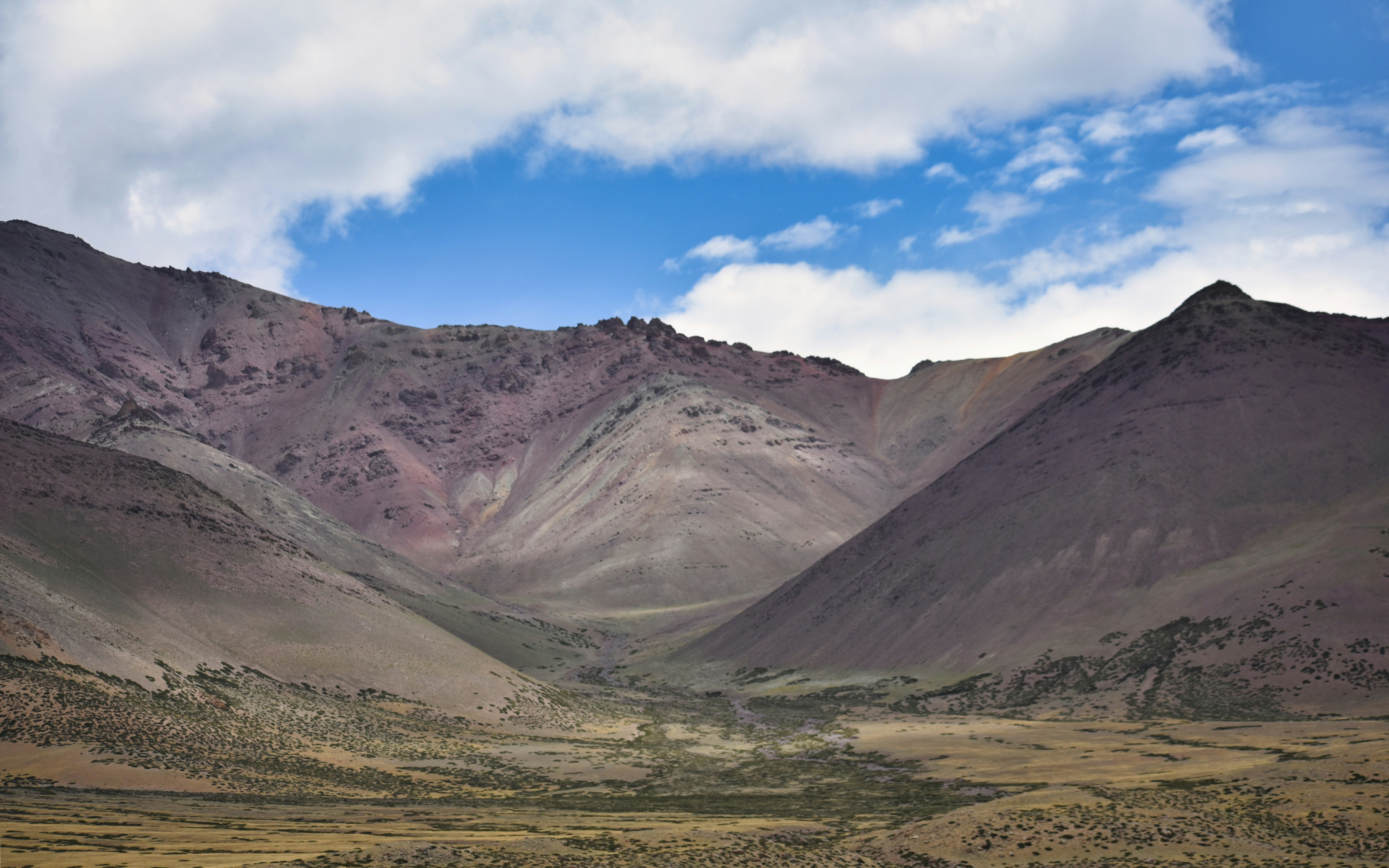 Barren mountainside with sparse vegetation under cloudy sky