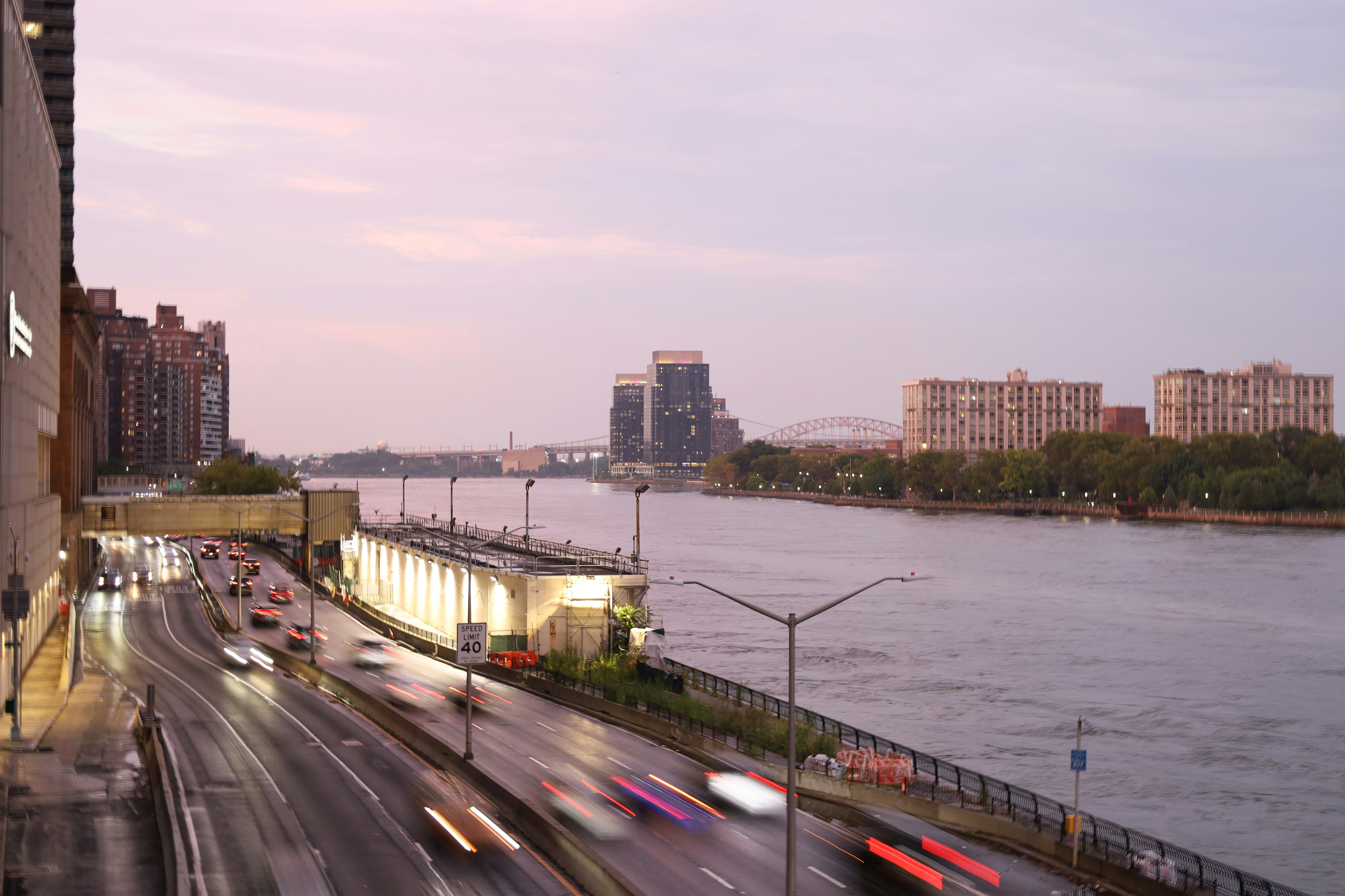 Dynamic view of a riverfront scene with flowing traffic and illuminated buildings under a twilight sky.