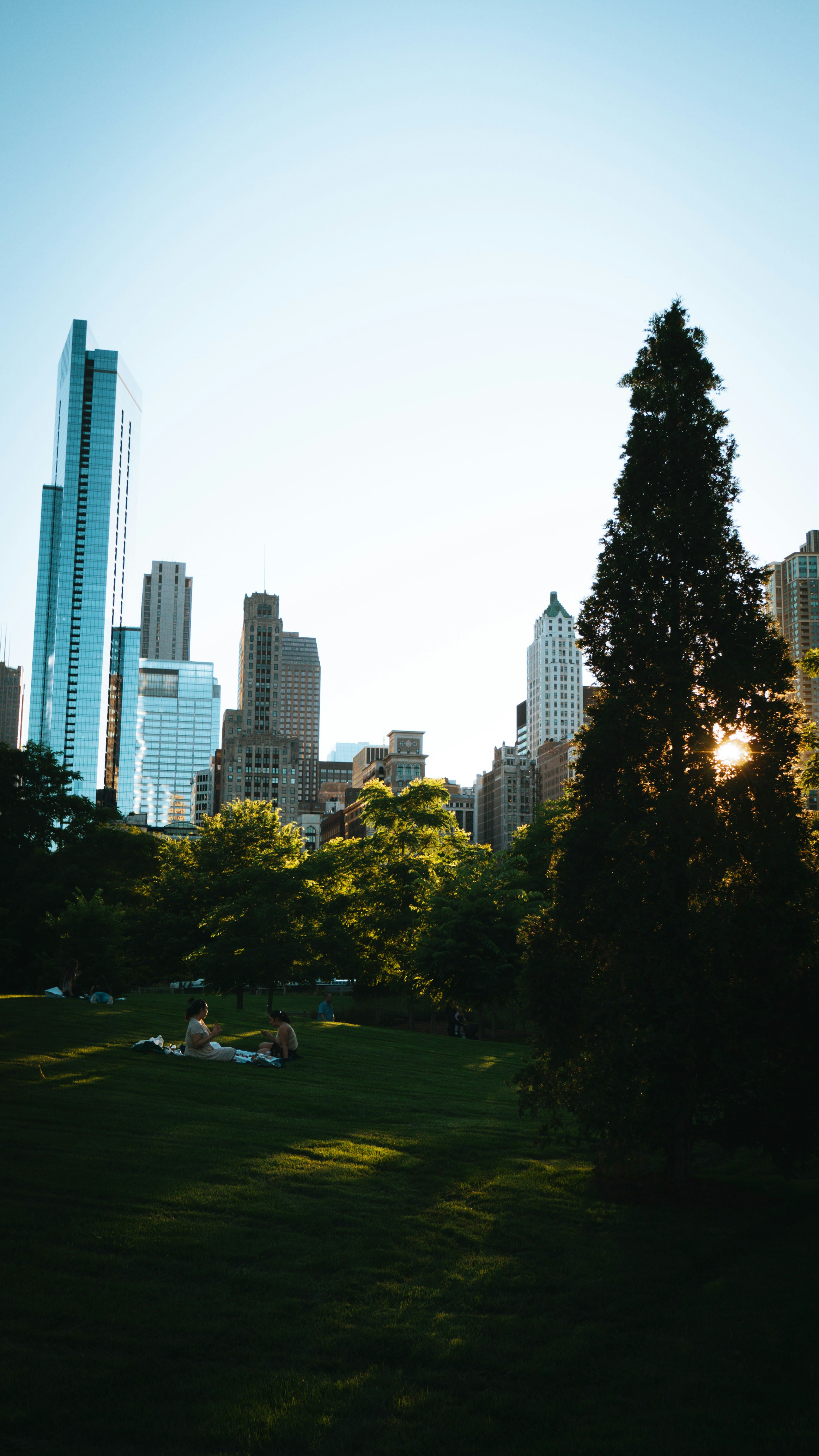 OLYMPUS DIGITAL CAMERA | People relaxing on a sunny day in a park with city skyline.