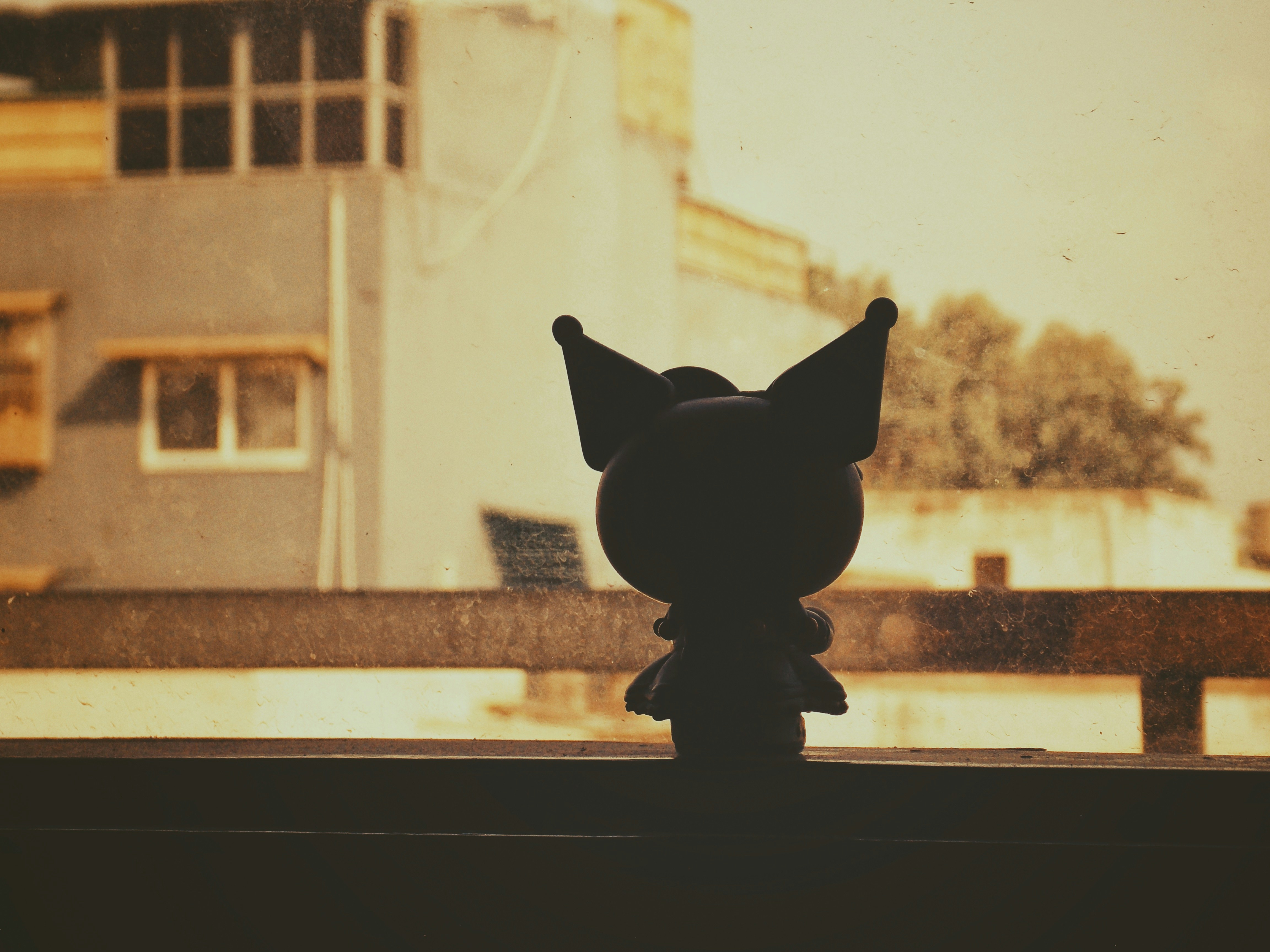 A moody silhouette of a toy figure placed on a window, with warm tones of sunset light and urban backdrop. Nostalgic and cinematic. | Silhouette of a small cartoon character facing away