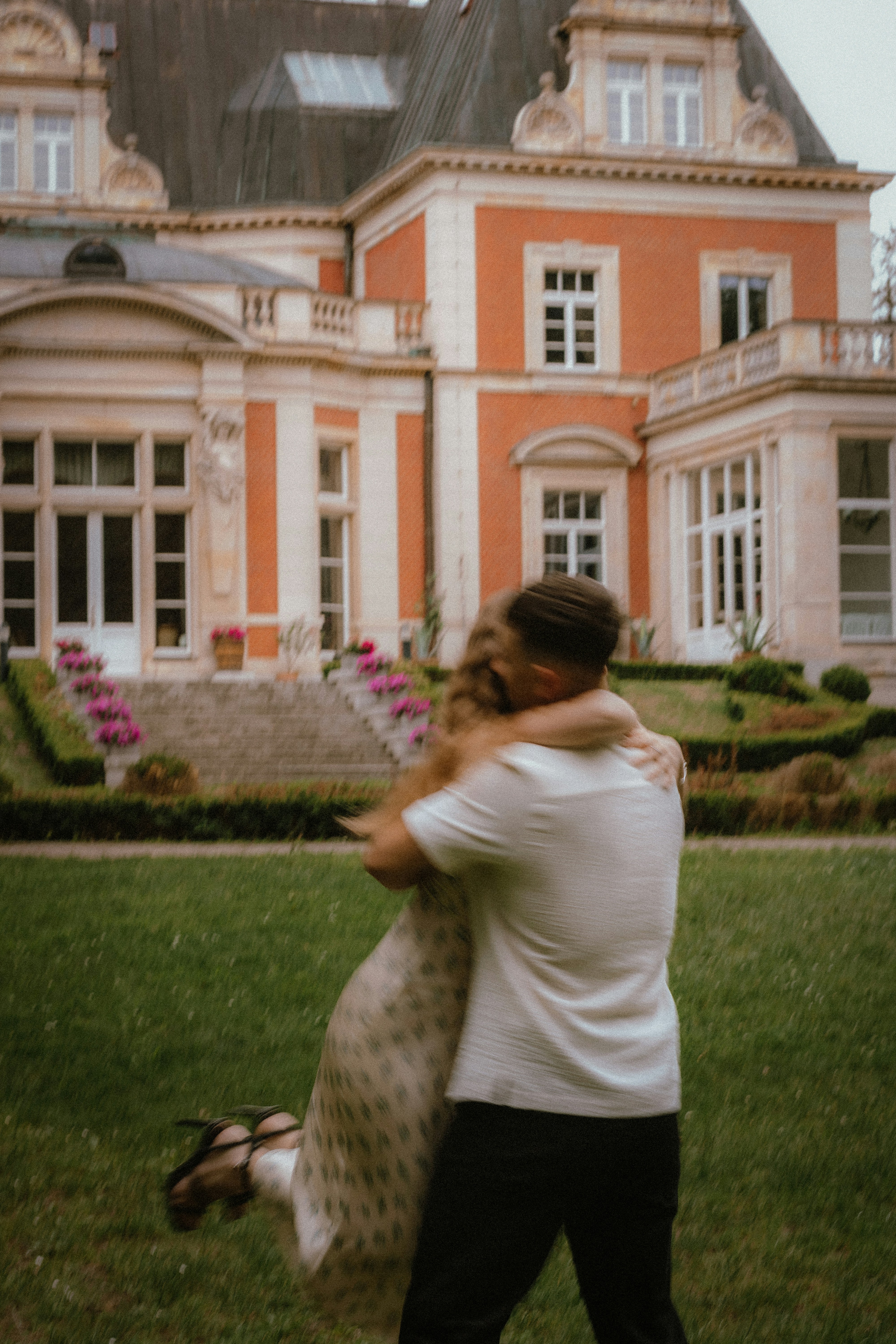 Couple embracing in front of a large brick building.