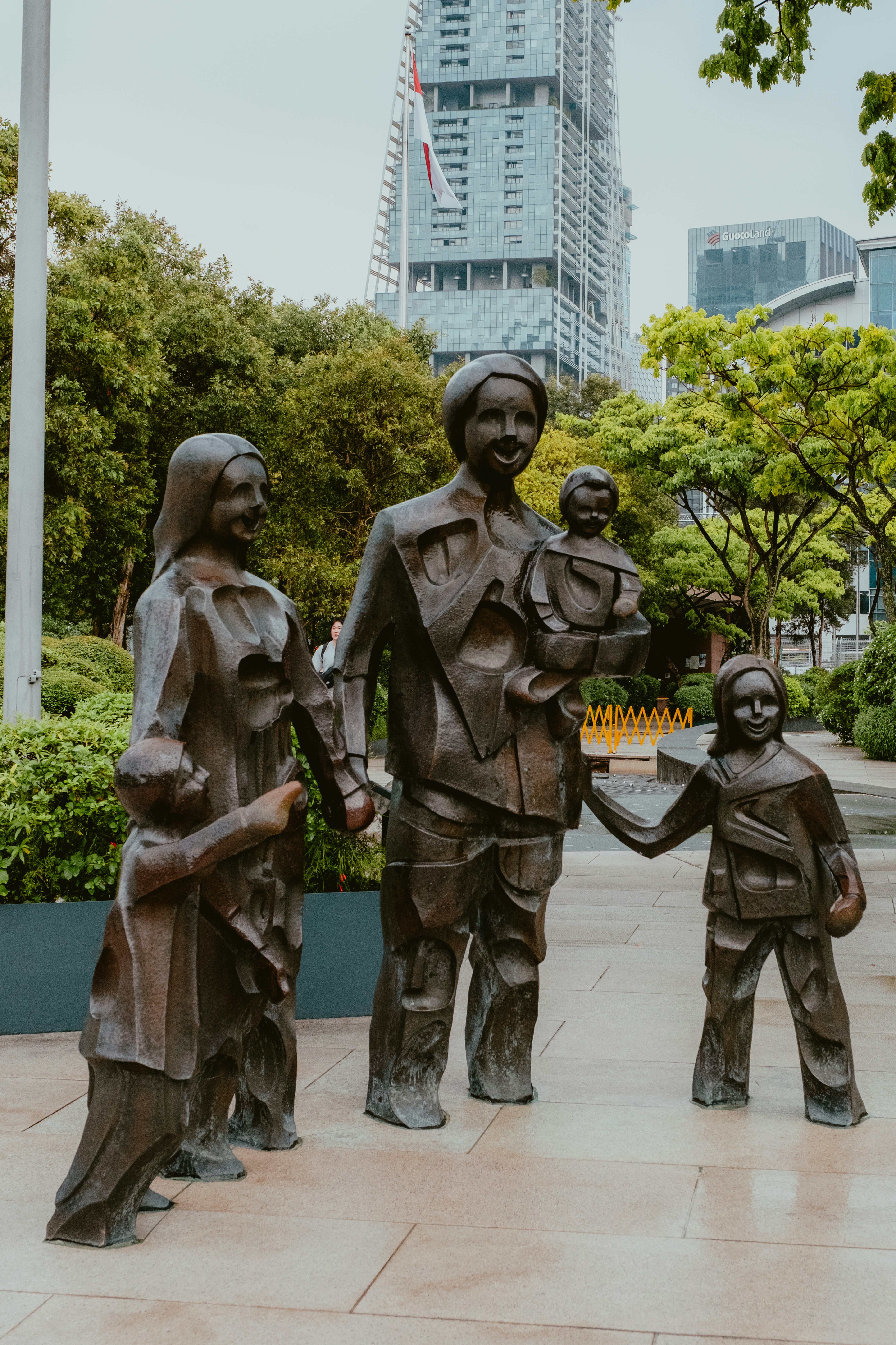 Bronze sculptures of a family holding hands, set against a backdrop of modern architecture and greenery.