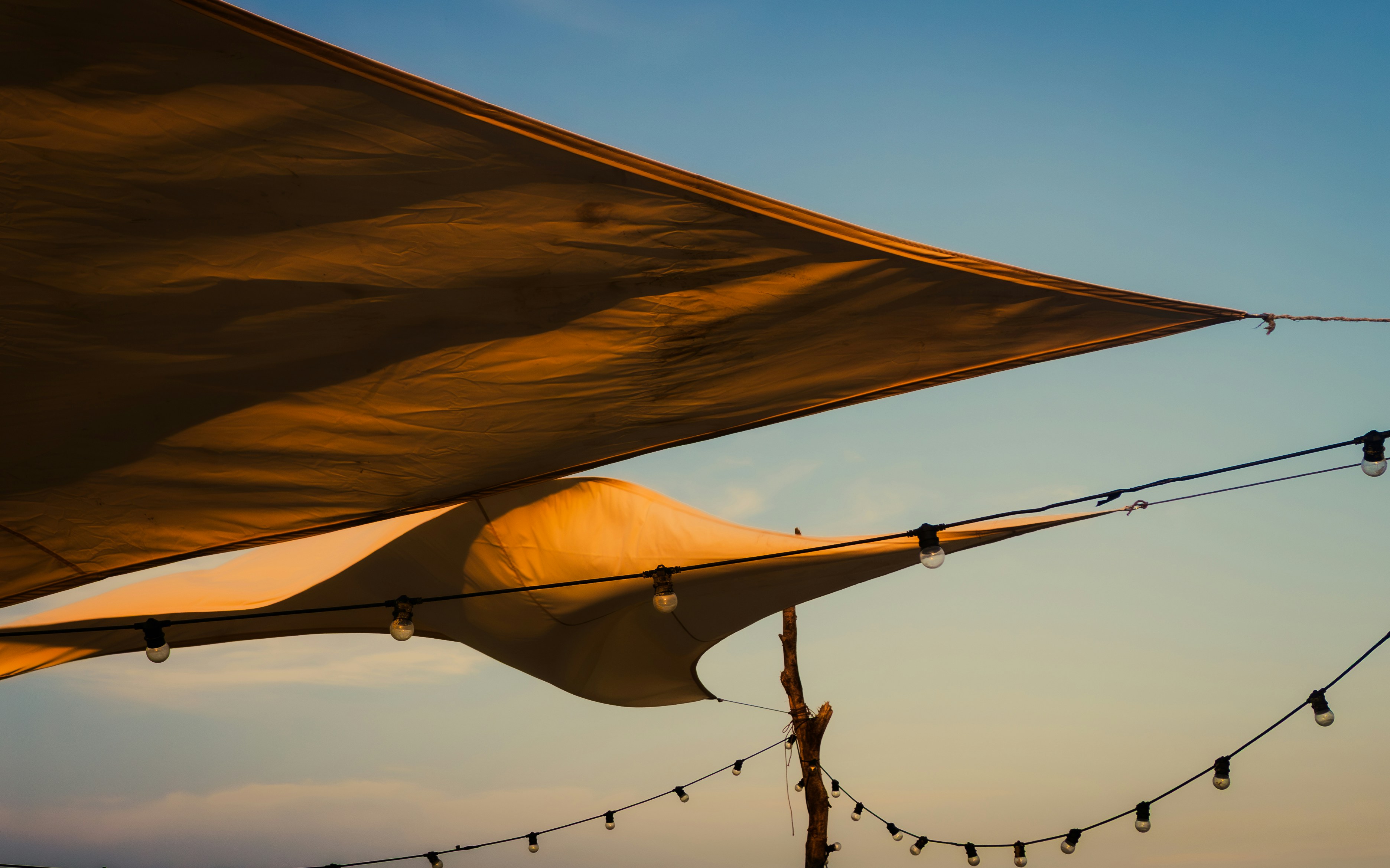 Elegant fabric canopies casting shadows against a twilight sky, illuminated by hanging lights. 