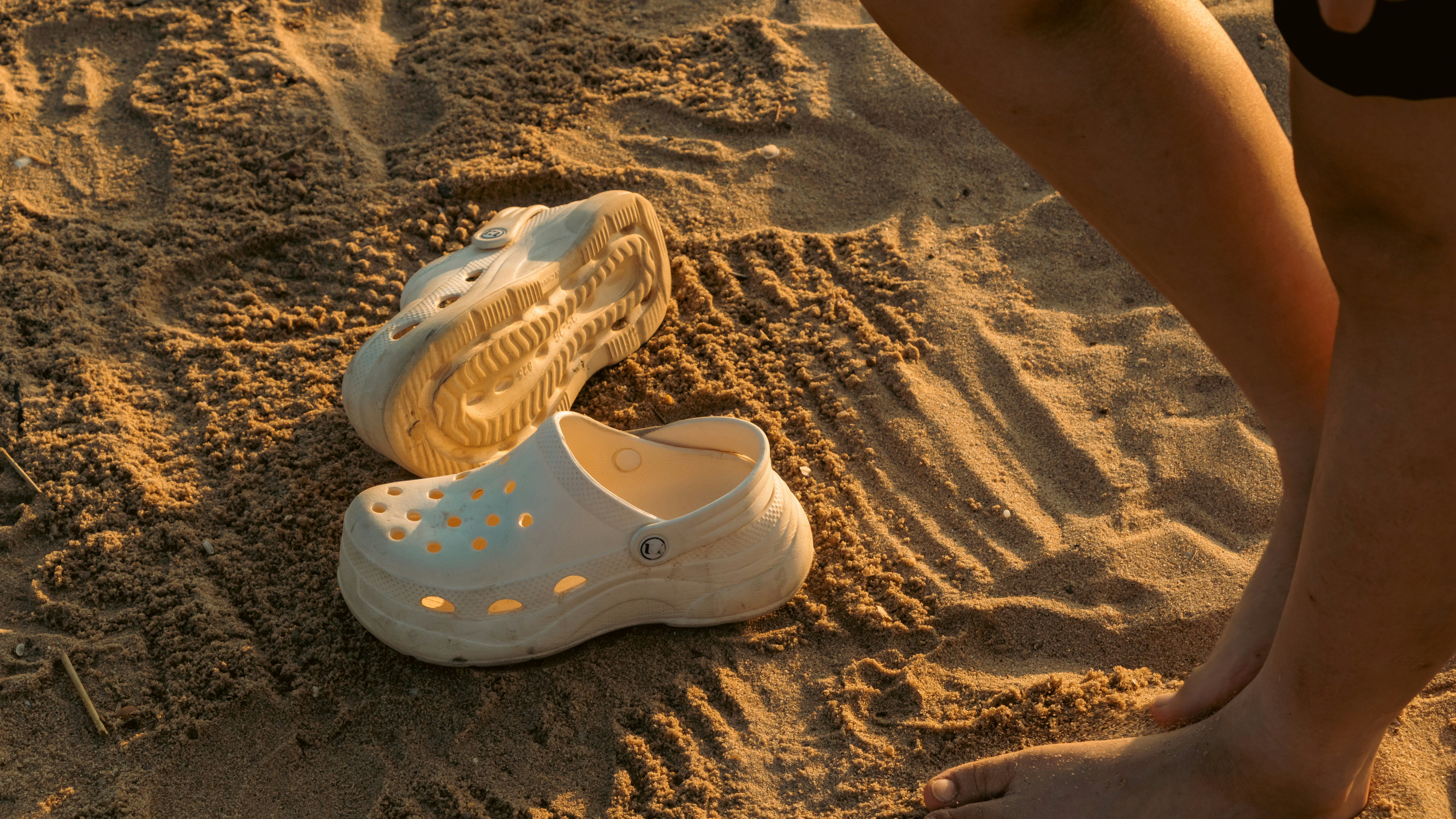 White clogs resting on sandy beach shore.