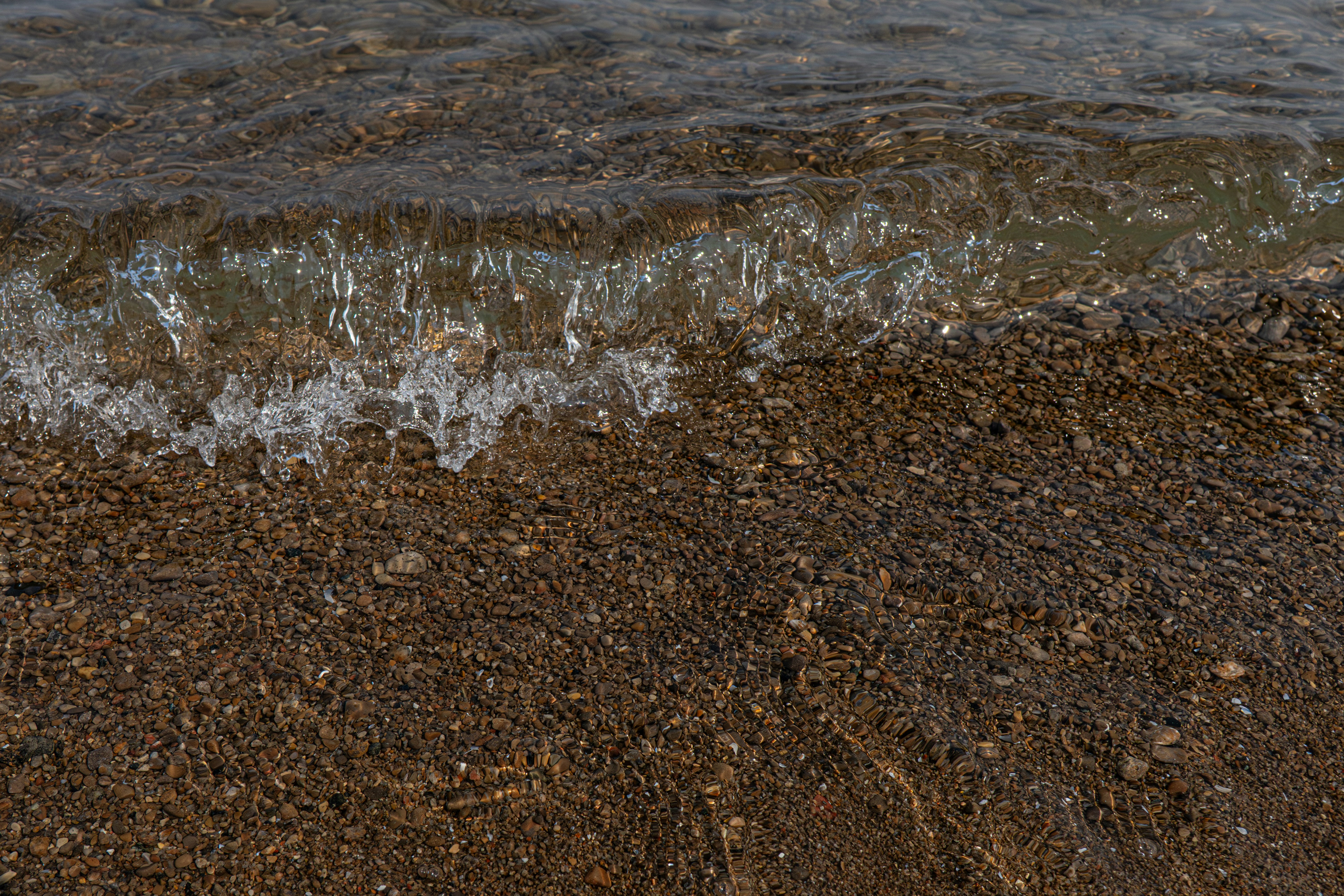 A nice shot of a small wave at Simcoe Lake beach at Sibbald Point Provincial Park | Gentle wave washes over a pebbly shore.