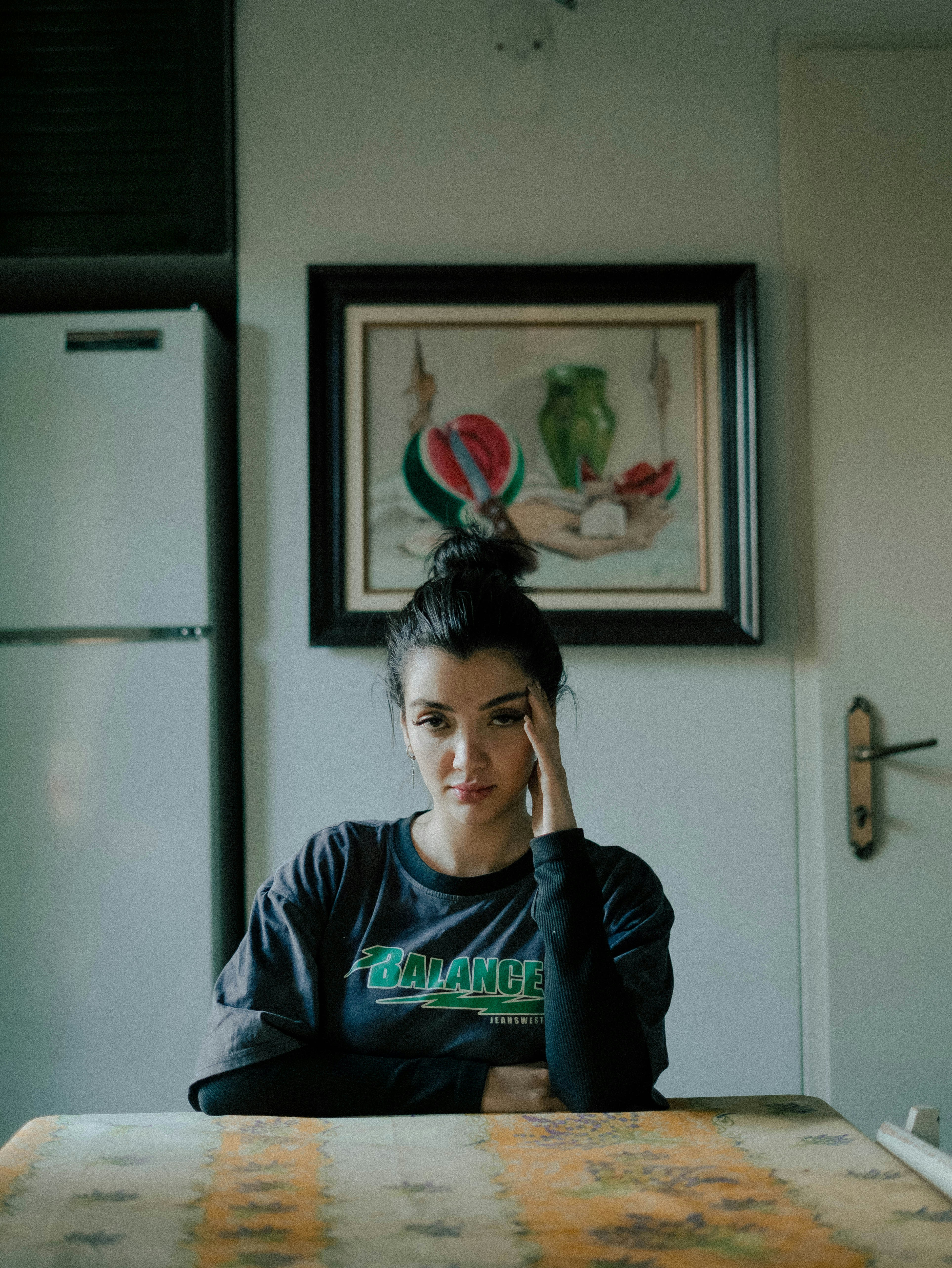 Young woman sits at a table with hand on head.
