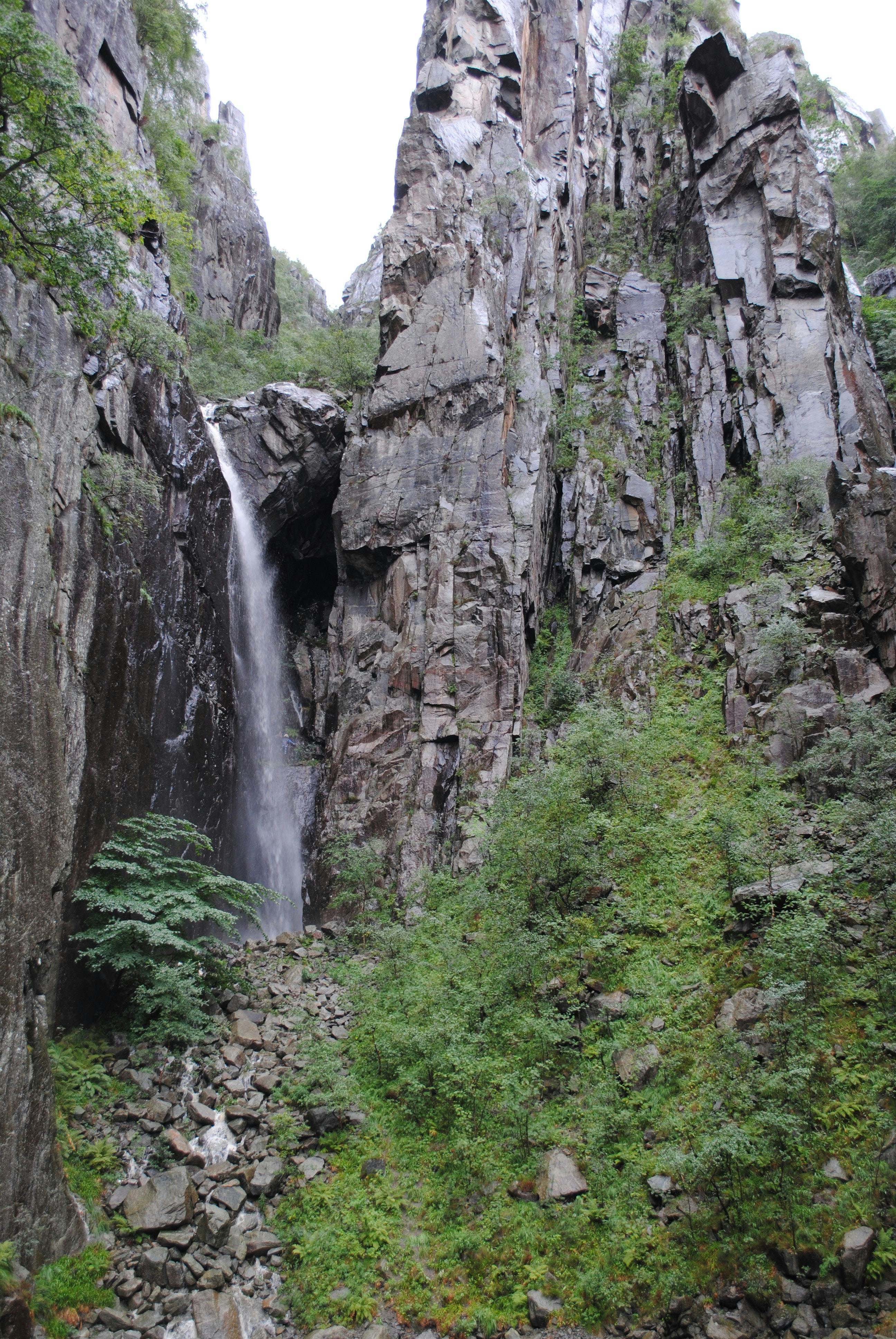 A majestic waterfall tumbles down rocky cliffs, surrounded by lush greenery and rugged stone formations.