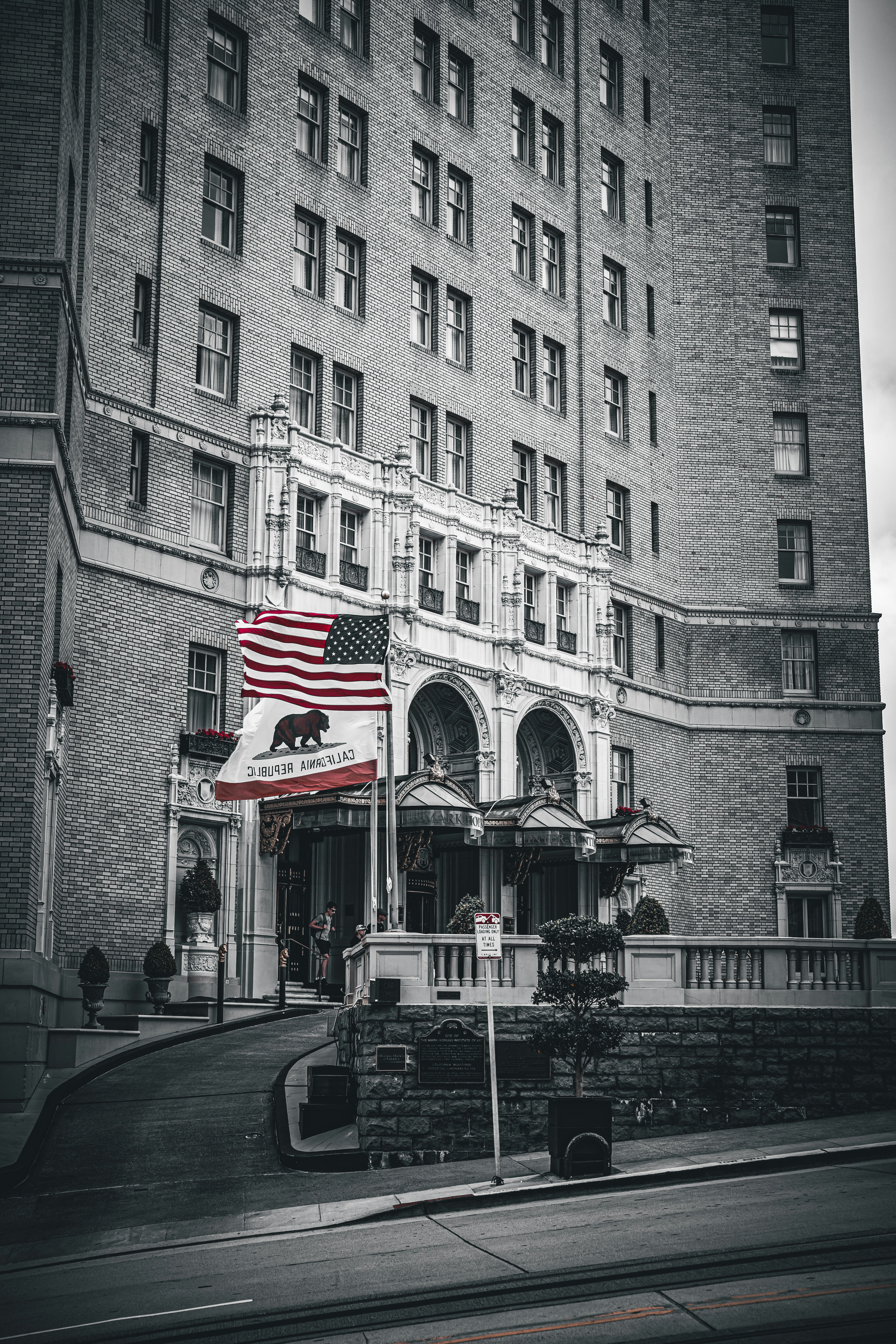 Historic hotel facade featuring the American and California flags, framed by elegant architectural details. The scene captures a blend of tradition and contemporary urban life.