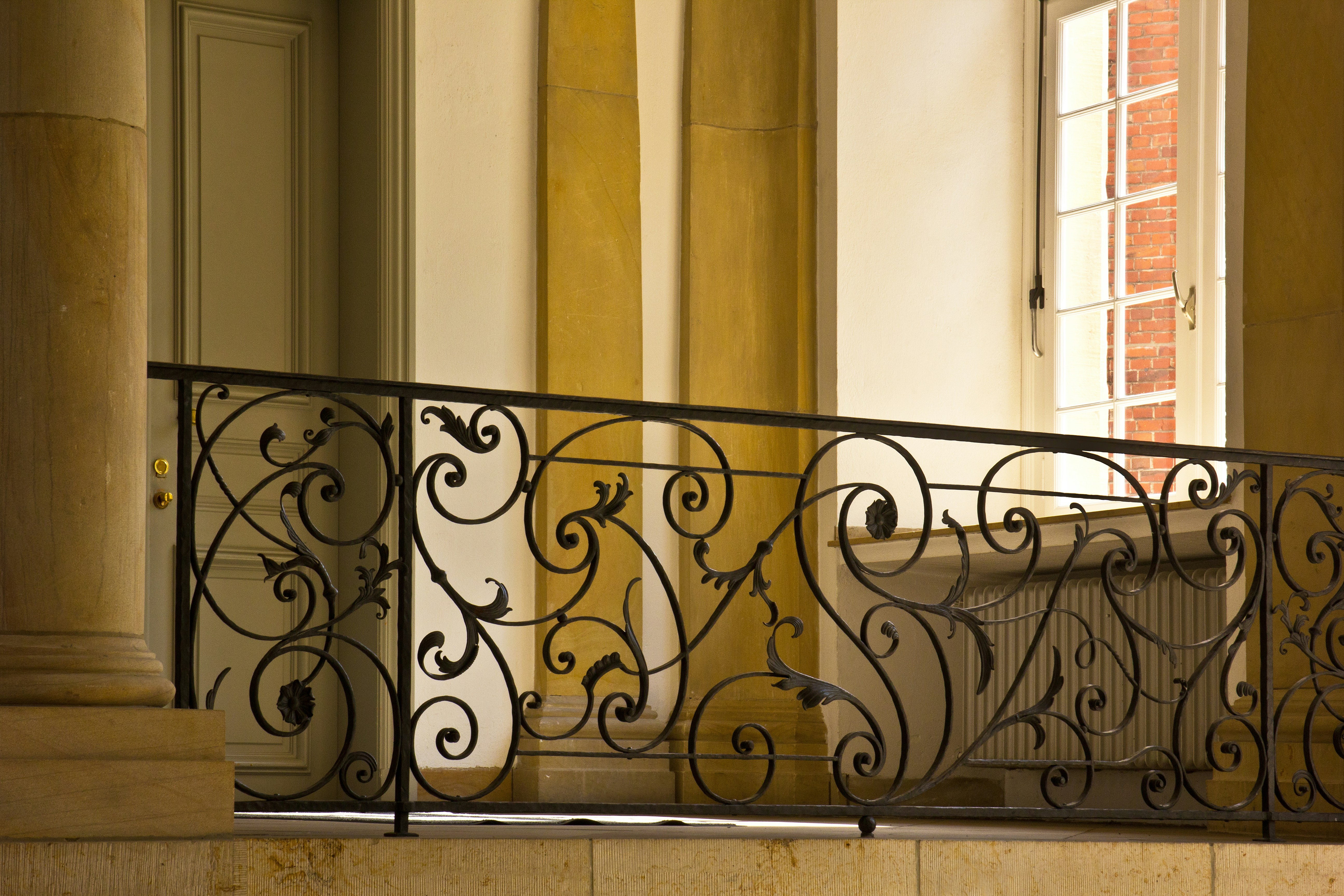 Ornate black metal railing in a sunlit hallway.