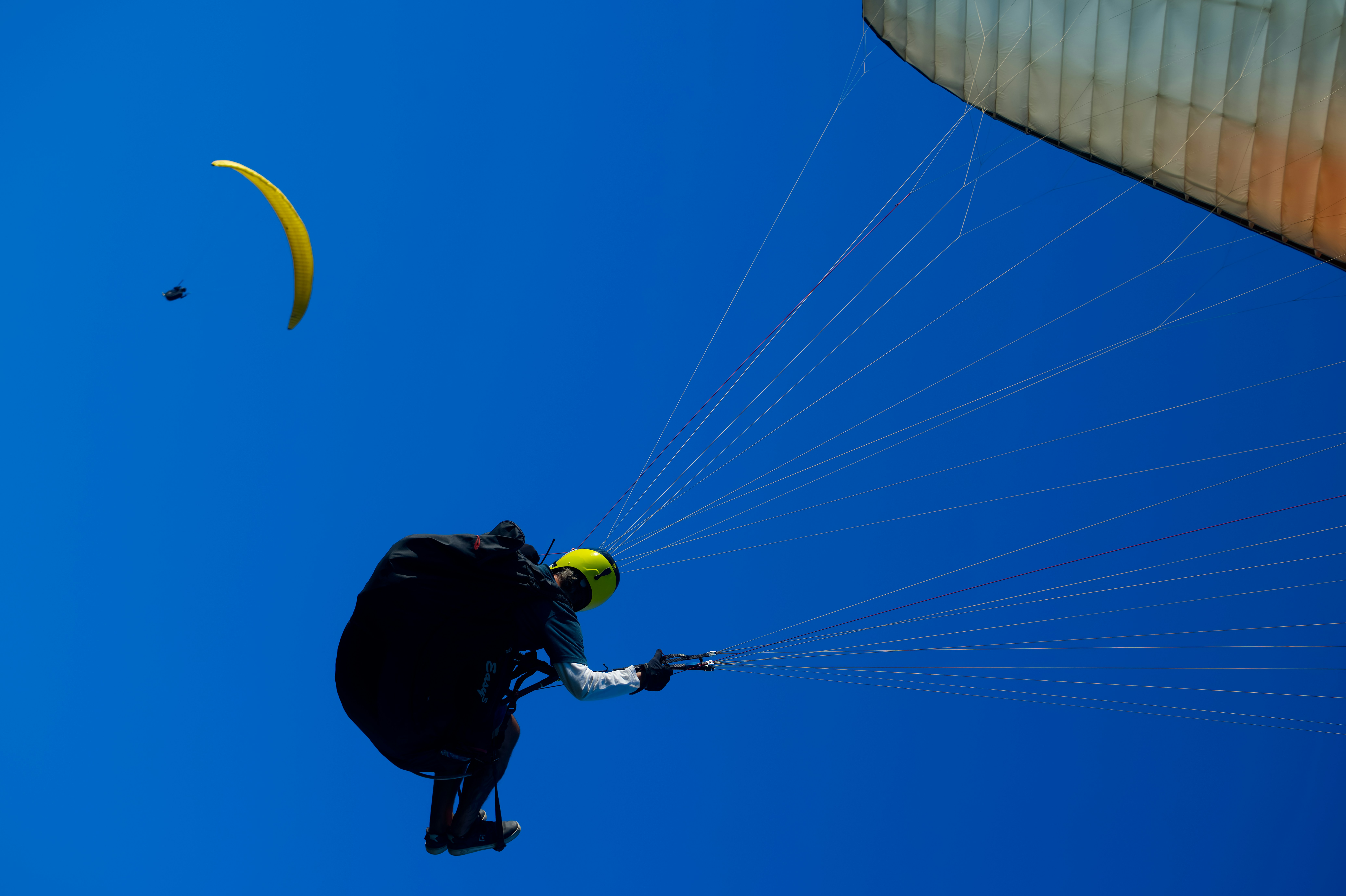 Azure Ascent: Yellow-helmeted Skydiver Grasping the Lines in a Crisp Blue Sky