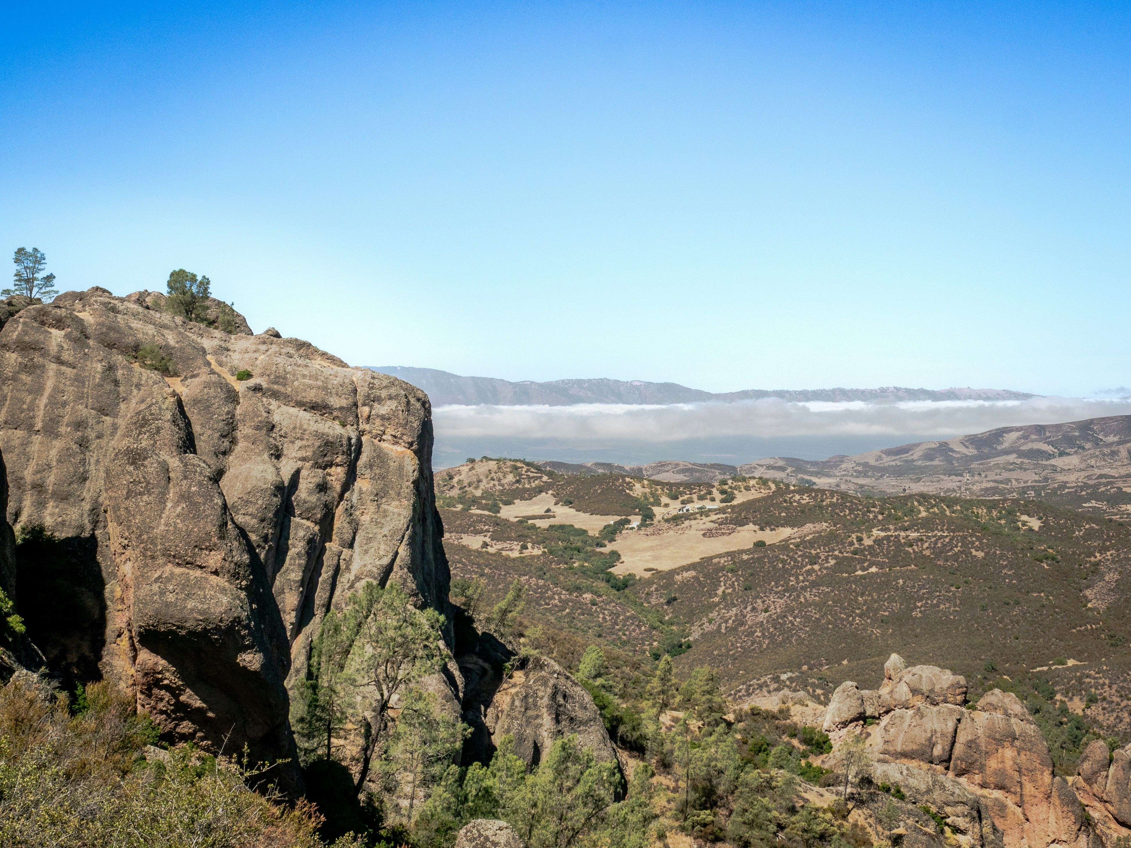 Majestic rocky formations overlook a vast landscape, with rolling hills and a misty horizon beyond. The scene captures nature's rugged beauty.