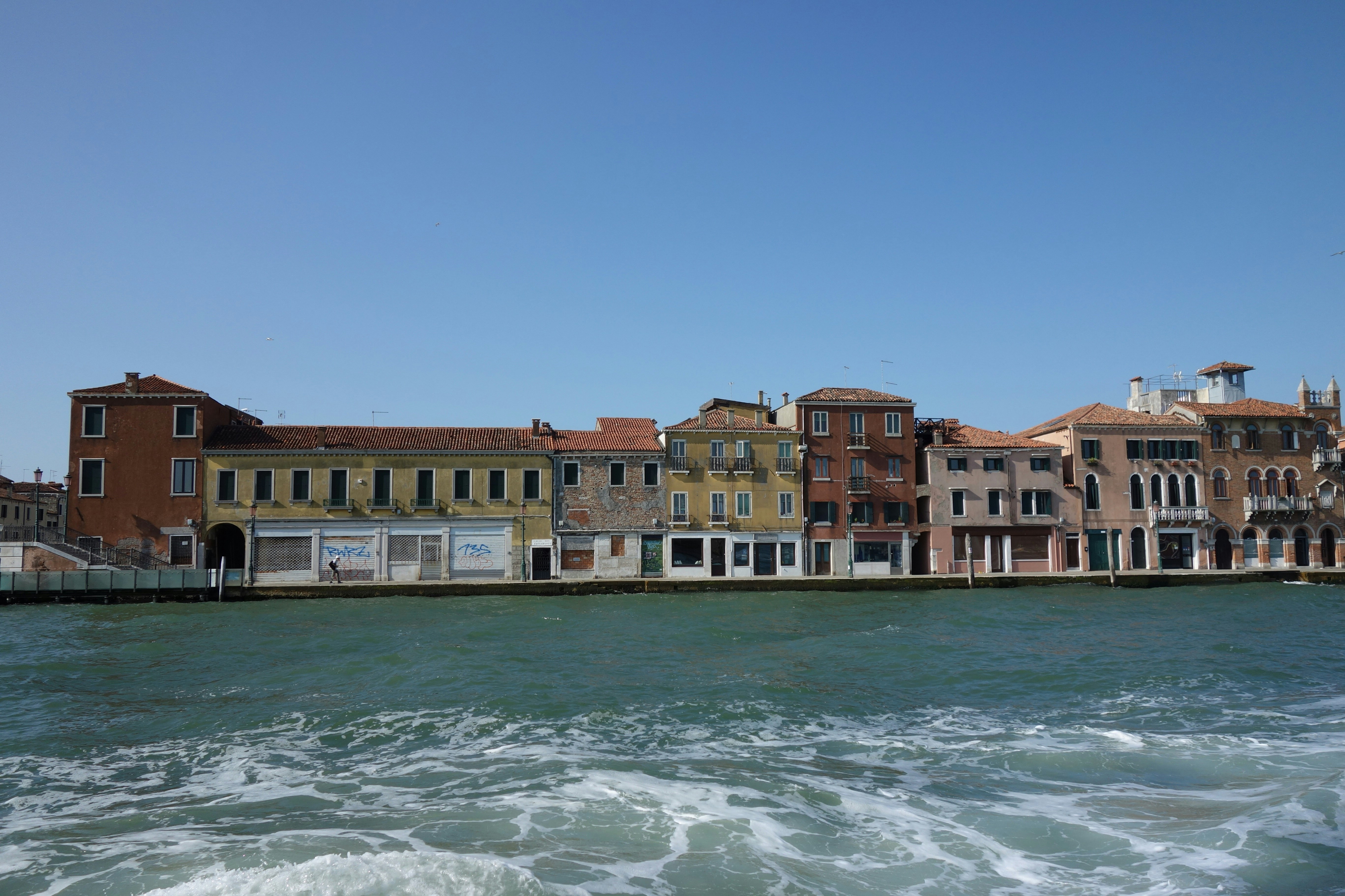 Colorful Venetian buildings lining the waterfront, showcasing architectural diversity against a clear blue sky.