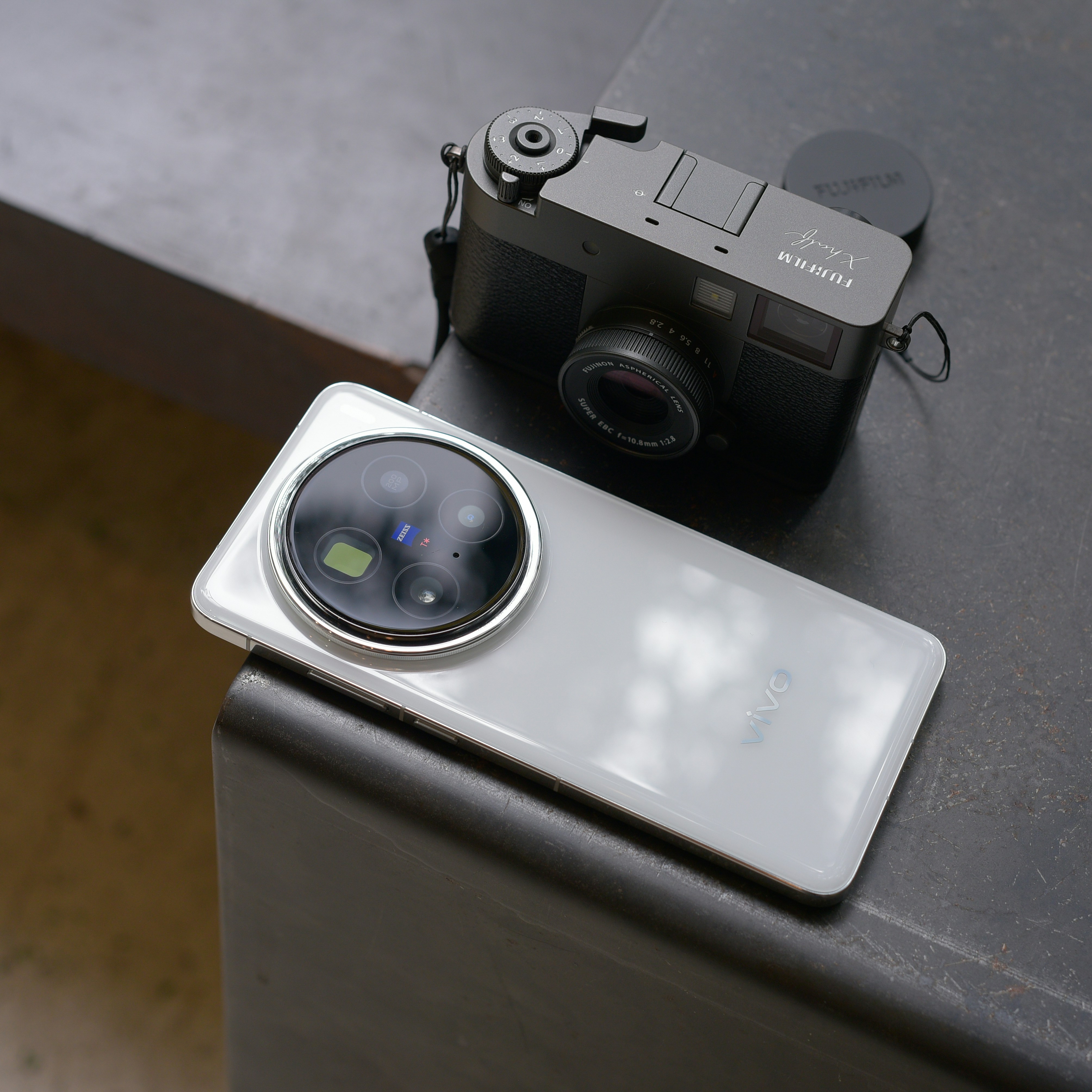 Vivo X200 Pro, Fujifilm Xhalf | Smartphone and camera resting on a dark surface.