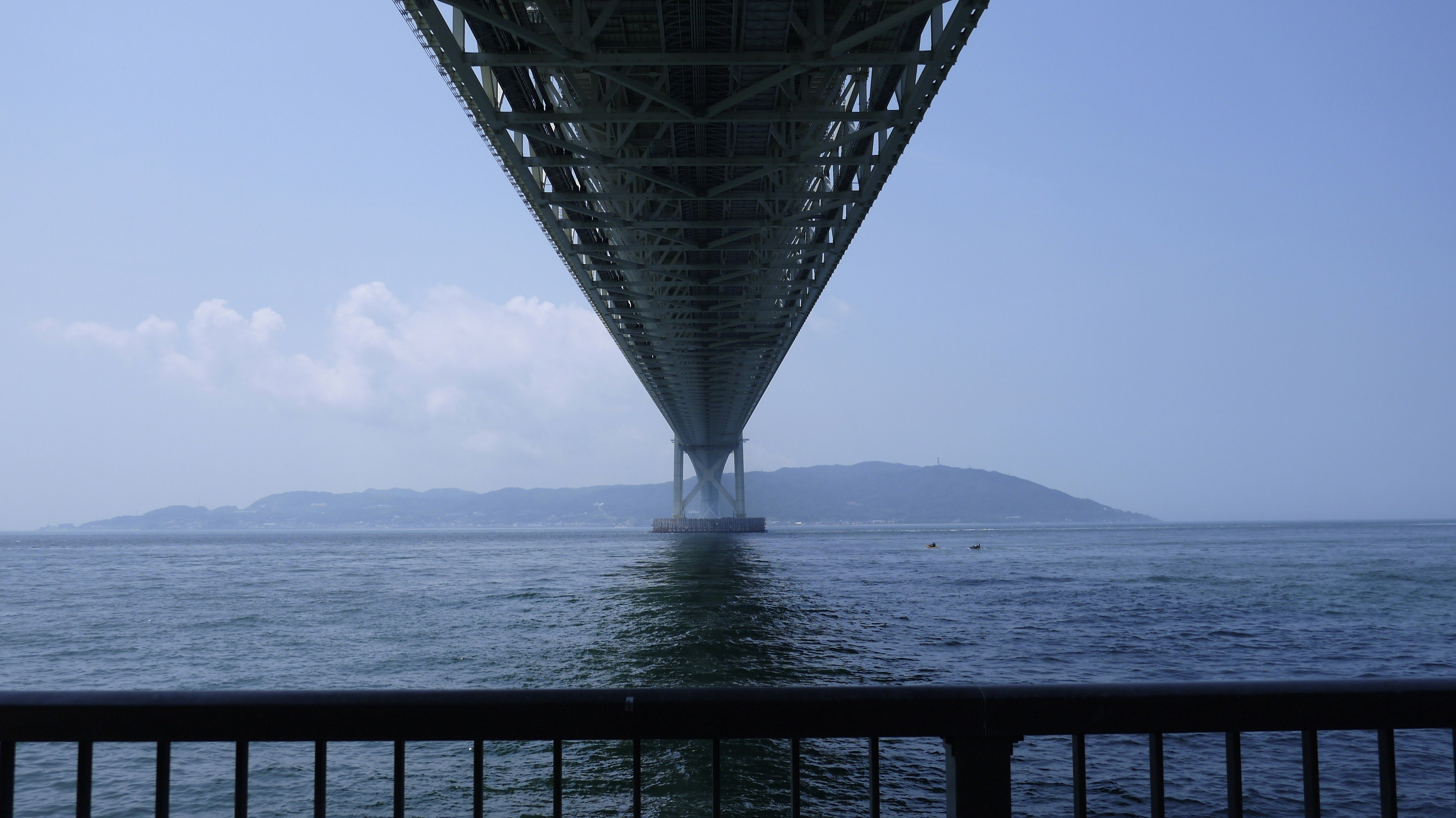 Underneath a large bridge with ocean and island.