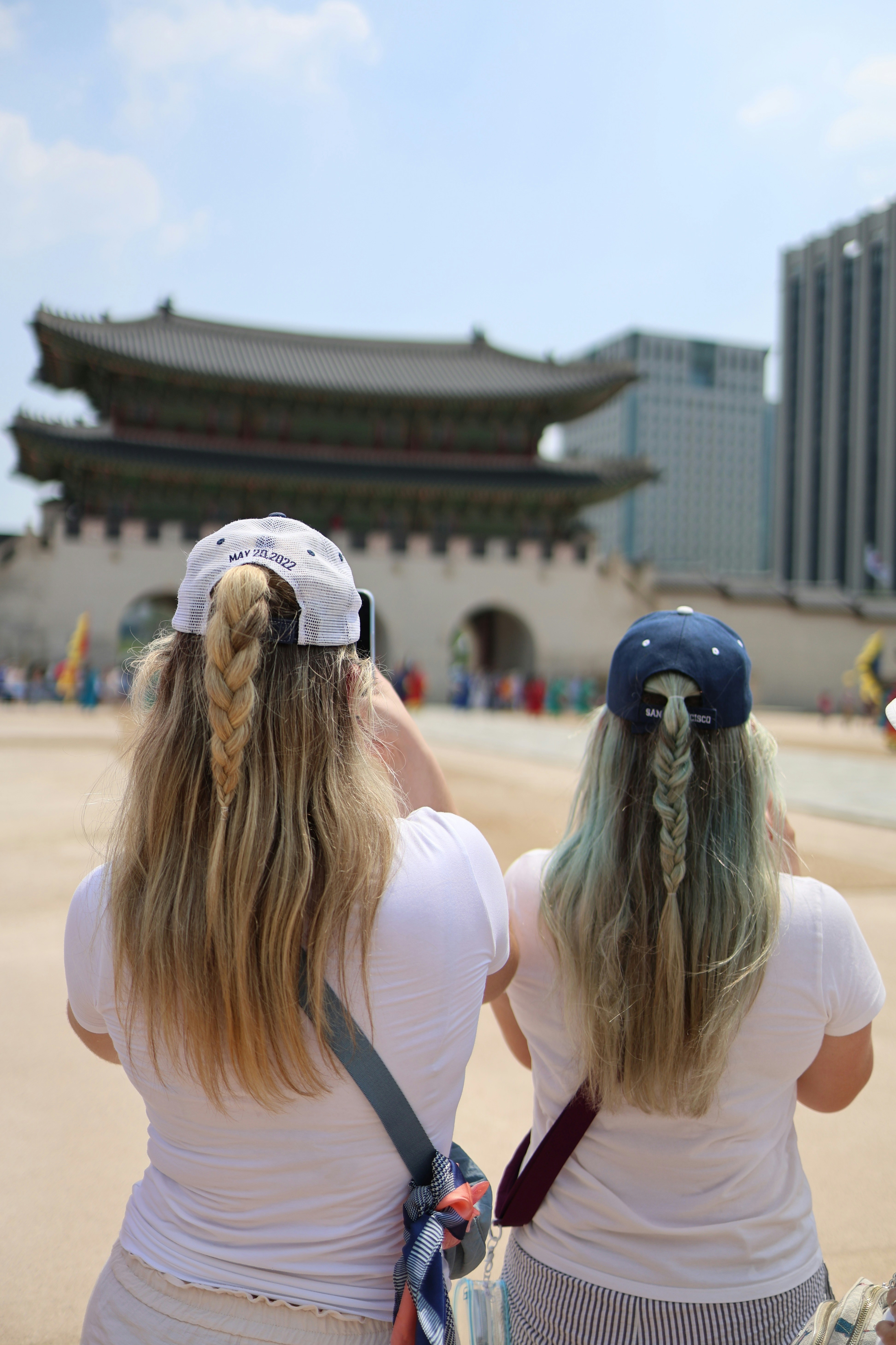 Two visitors admiring the architectural beauty of Gyeongbokgung Palace, framed by modern skyscrapers in the background.