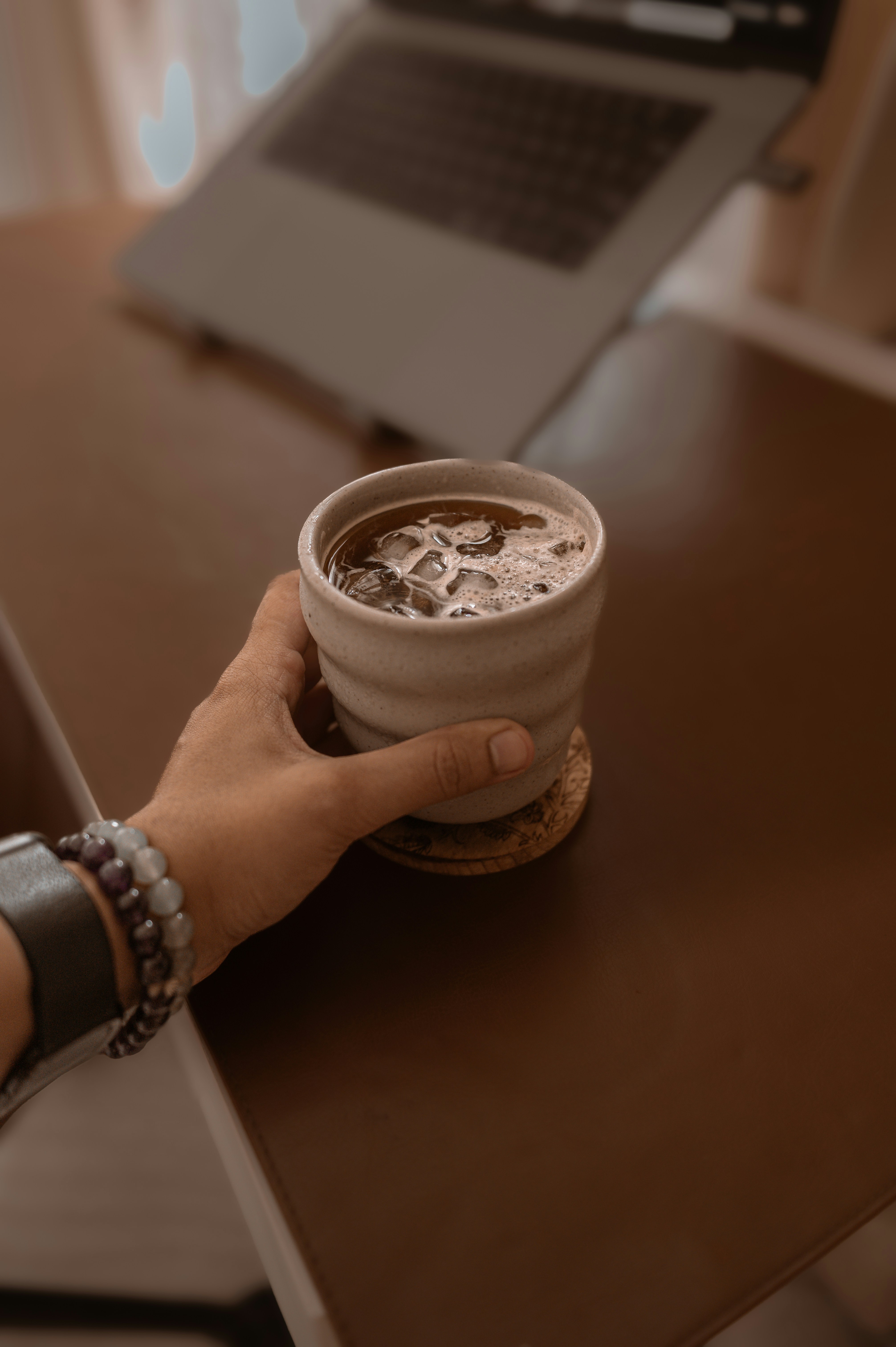 Hand holding a cup of iced coffee next to laptop