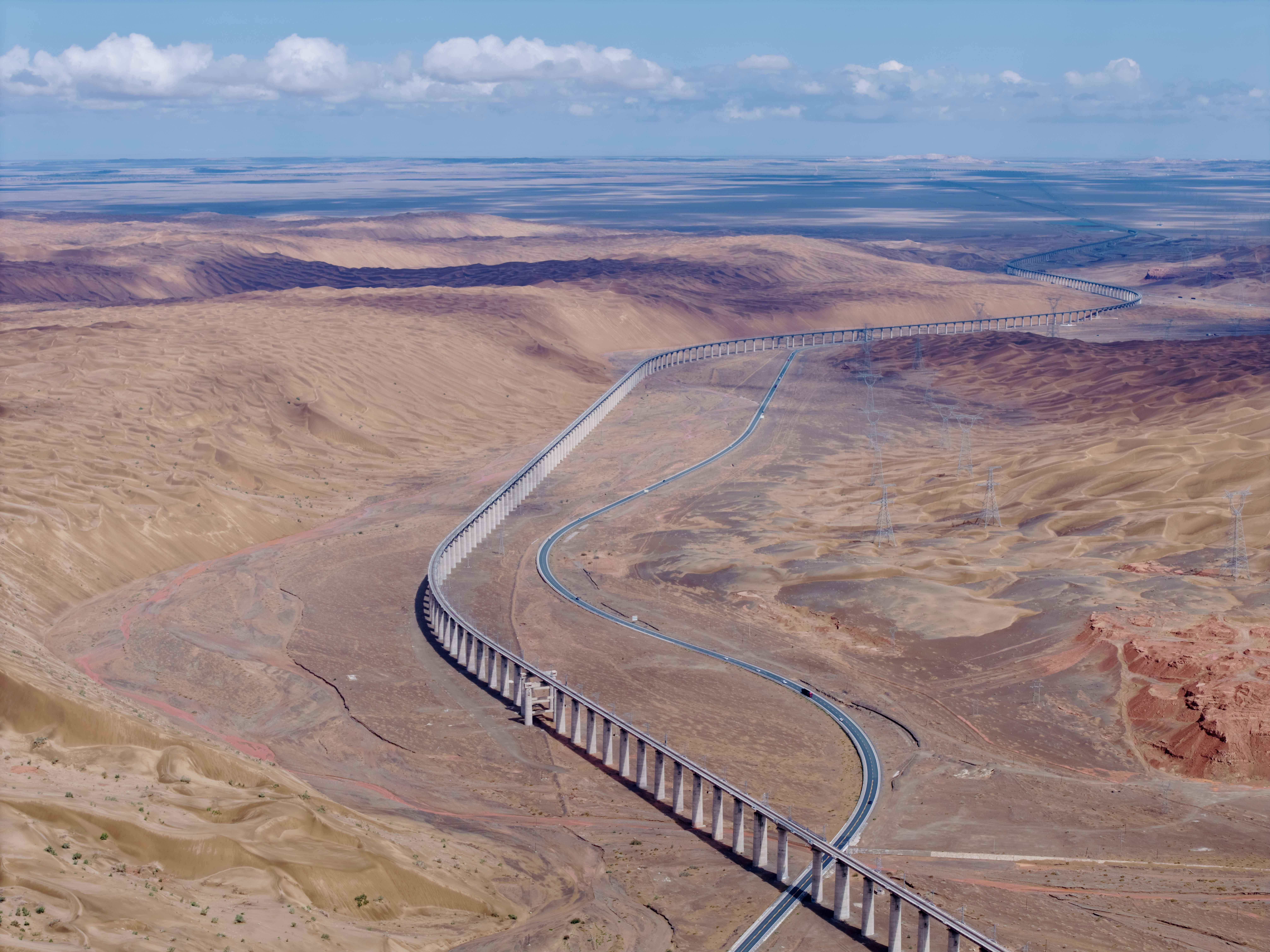Across a boundless land, a rainbow of steel takes flight—a testament to human will over the vast wilderness, an epic of strength and ambition. | Long railway viaduct crossing arid desert landscape