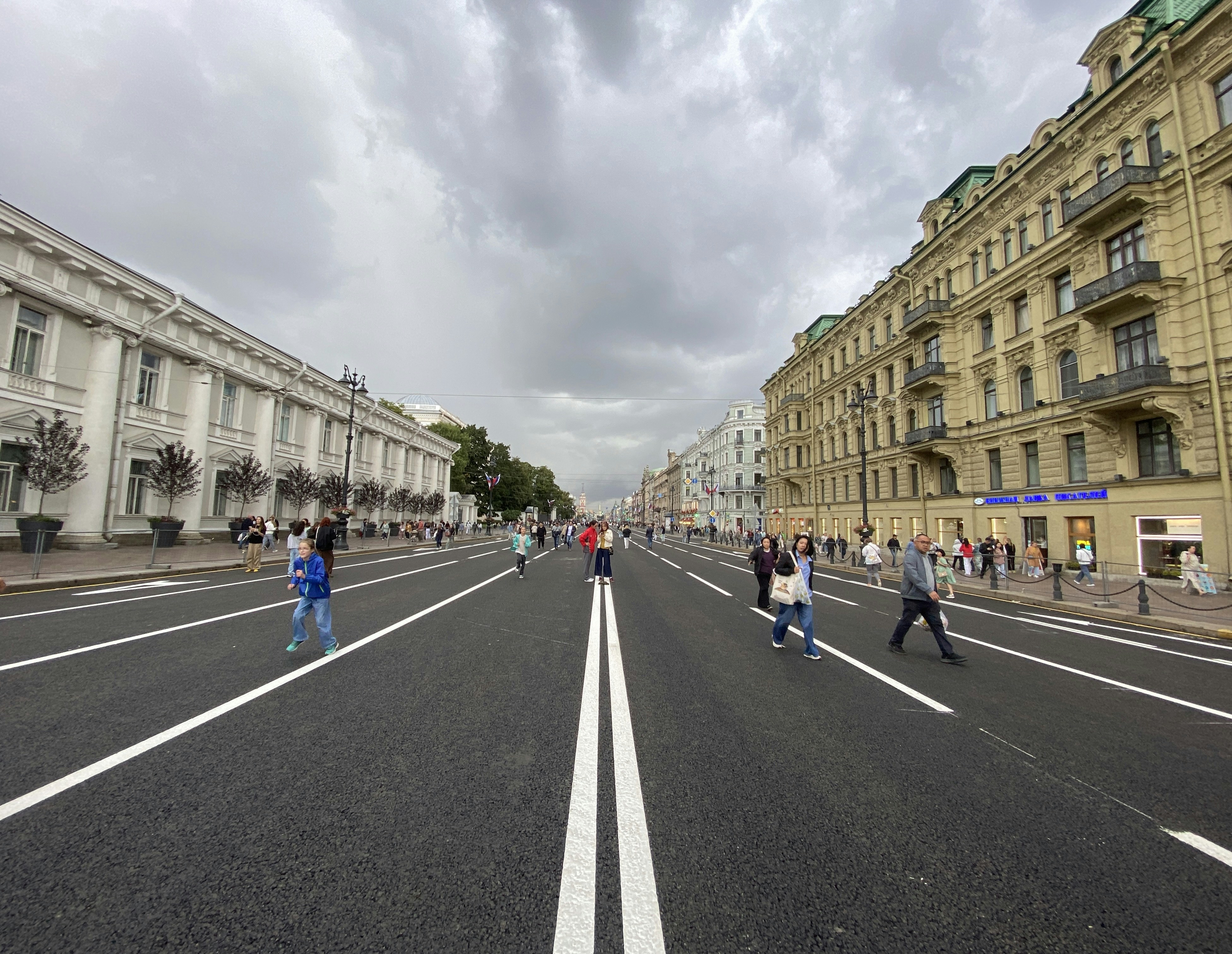 Bustling city street with pedestrians crossing under a moody sky, showcasing a blend of modern and historical architecture.