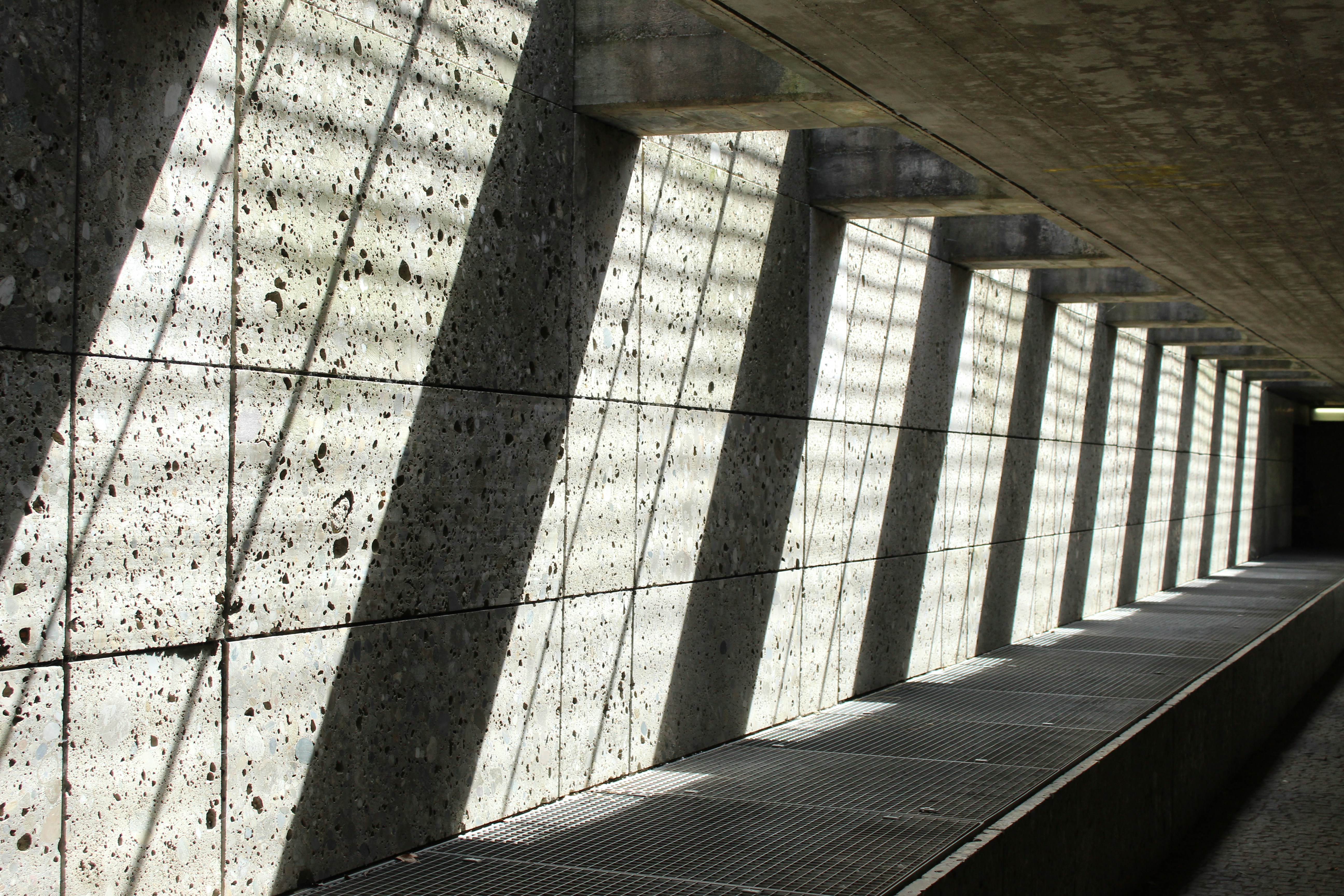 Diagonal beams of light cast striking shadows on textured concrete walls, creating a dynamic interplay of light and form.
