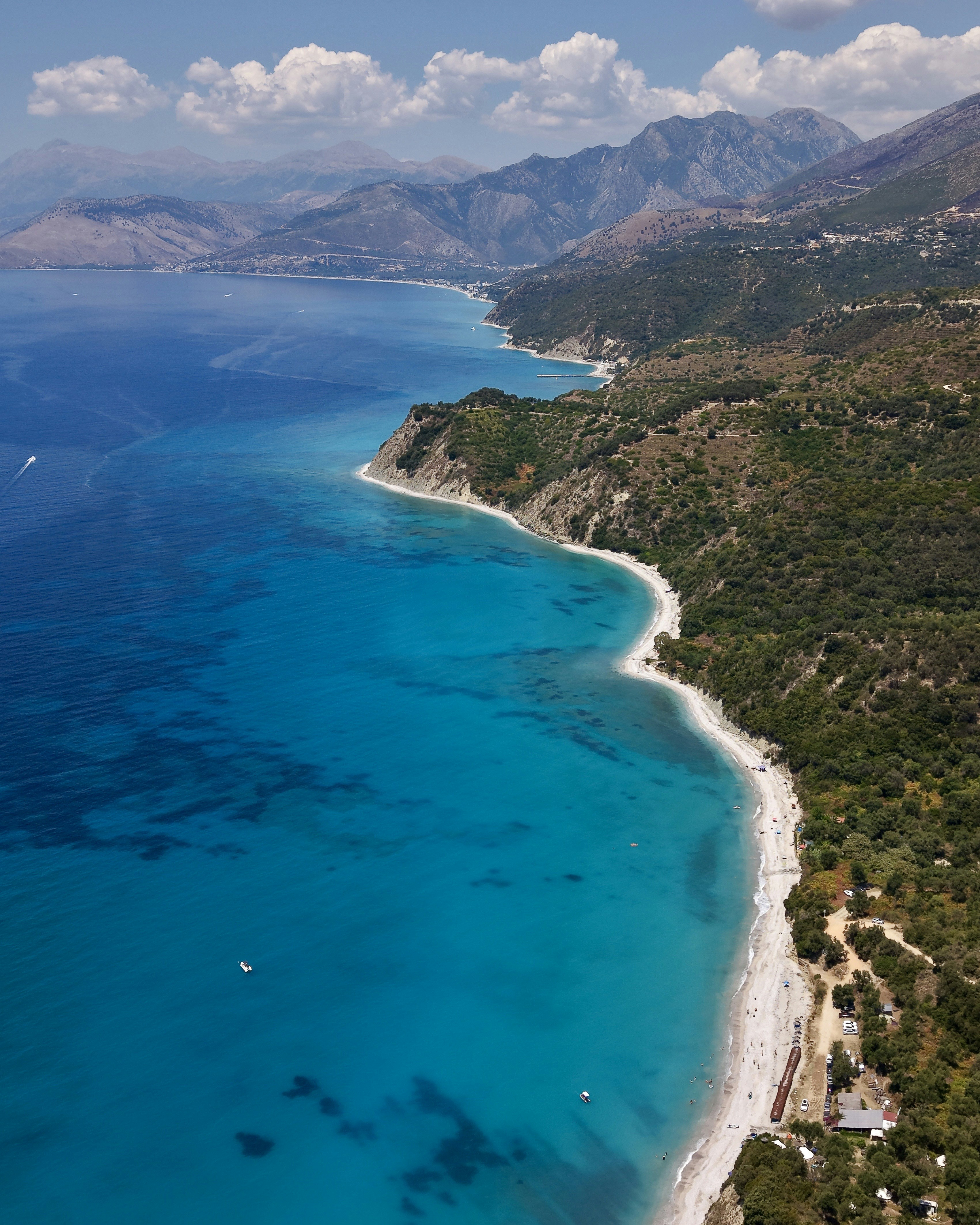 Aerial view of a picturesque coastline where turquoise waters meet lush greenery, revealing sandy beaches and gentle waves. The scene captures the harmonious blend of nature's colors.