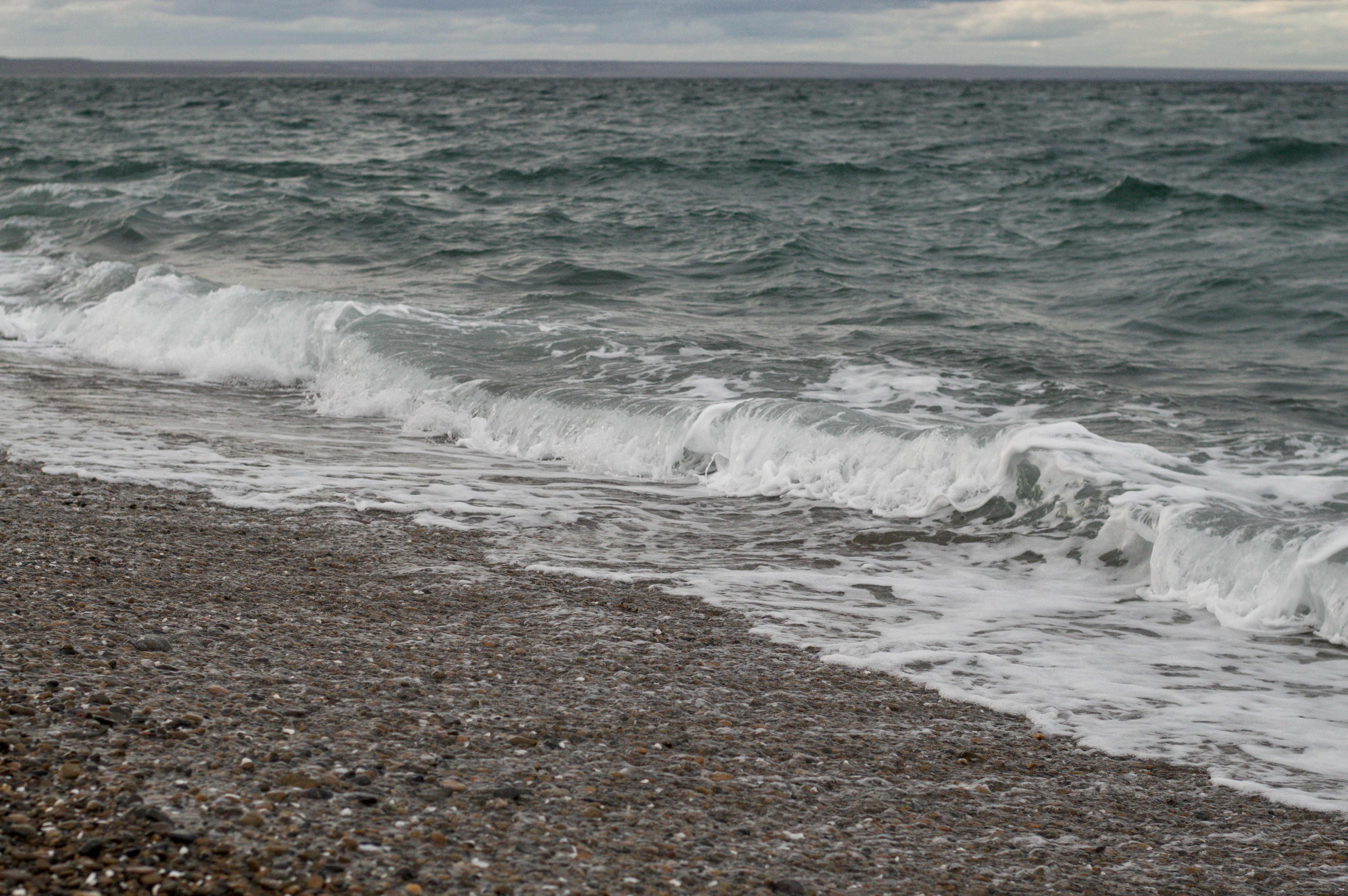 Waves crash on a pebble beach under cloudy skies