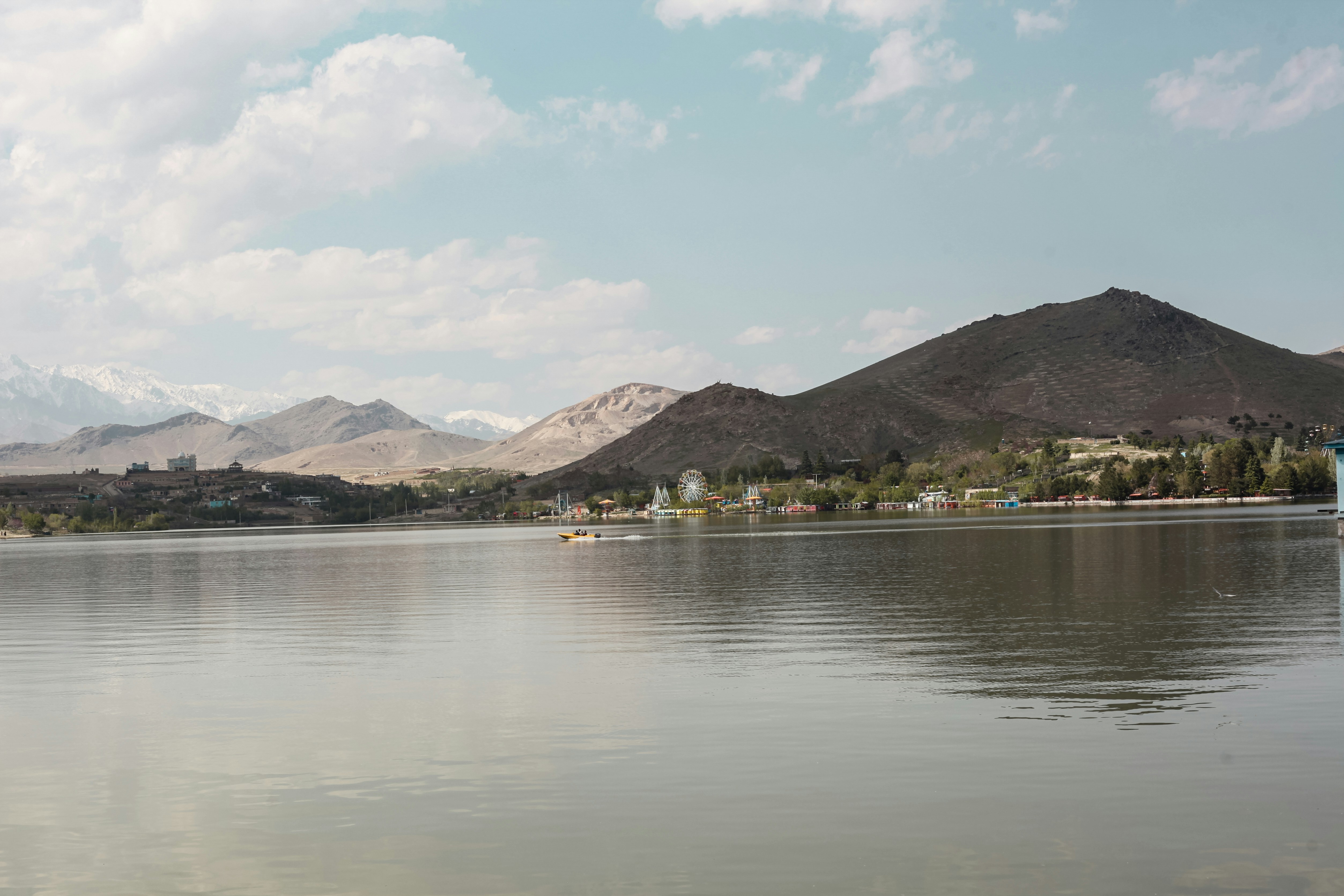 Tranquil lake reflecting surrounding mountains and a distant village under a cloudy sky.