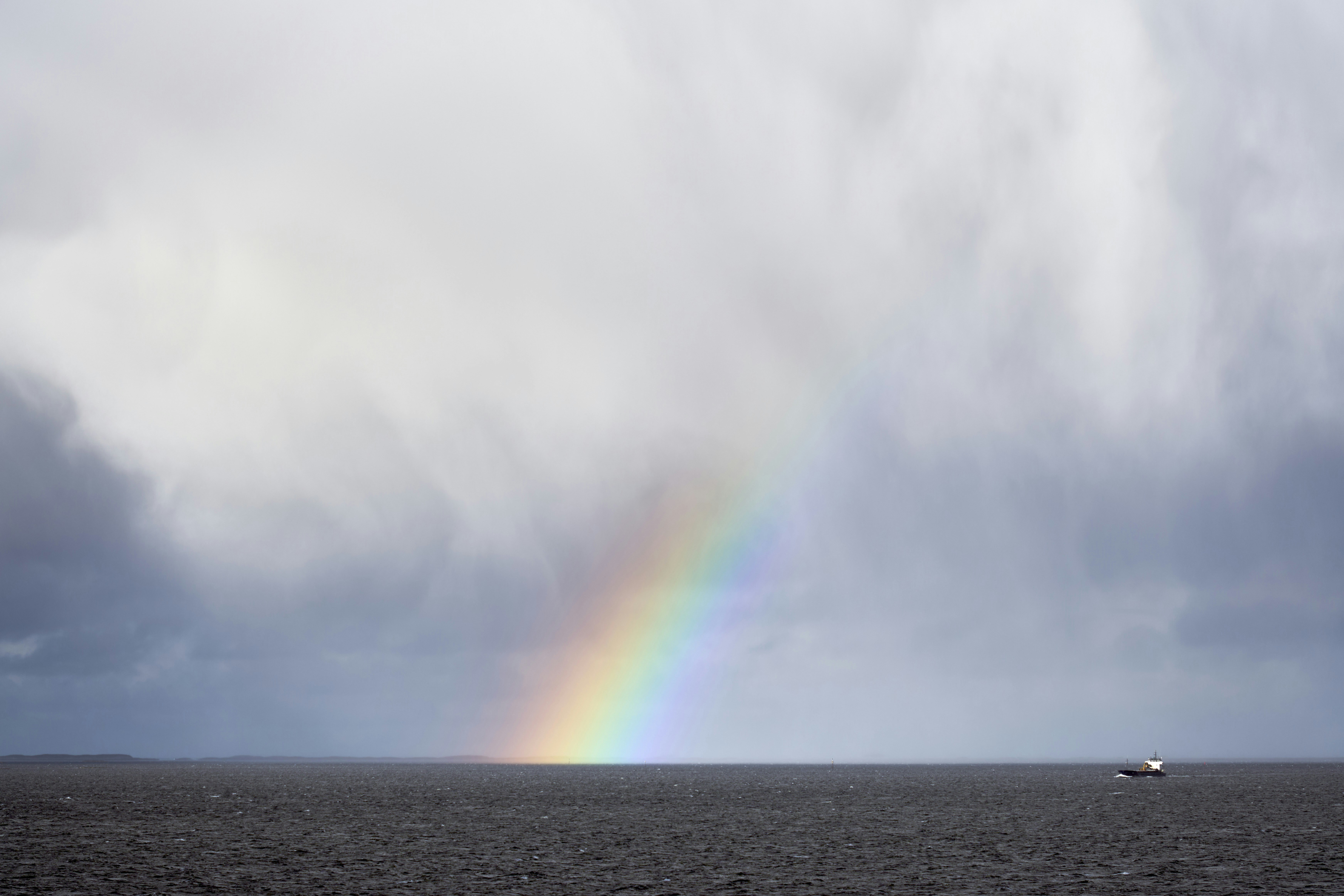 Rainbow over the dark ocean with a distant boat.