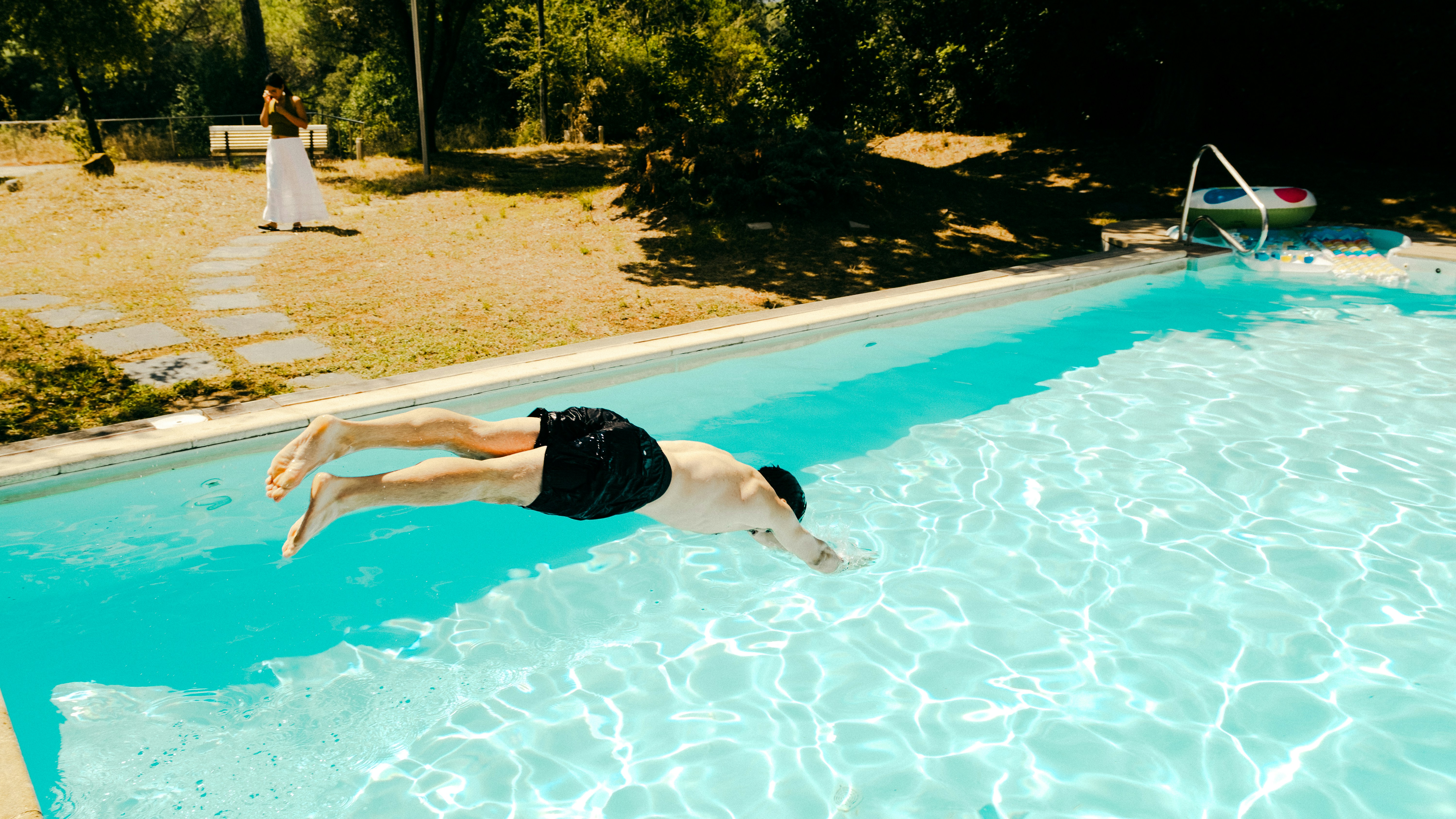 to the water duck (al agua pato) | Man dives into a bright blue swimming pool.