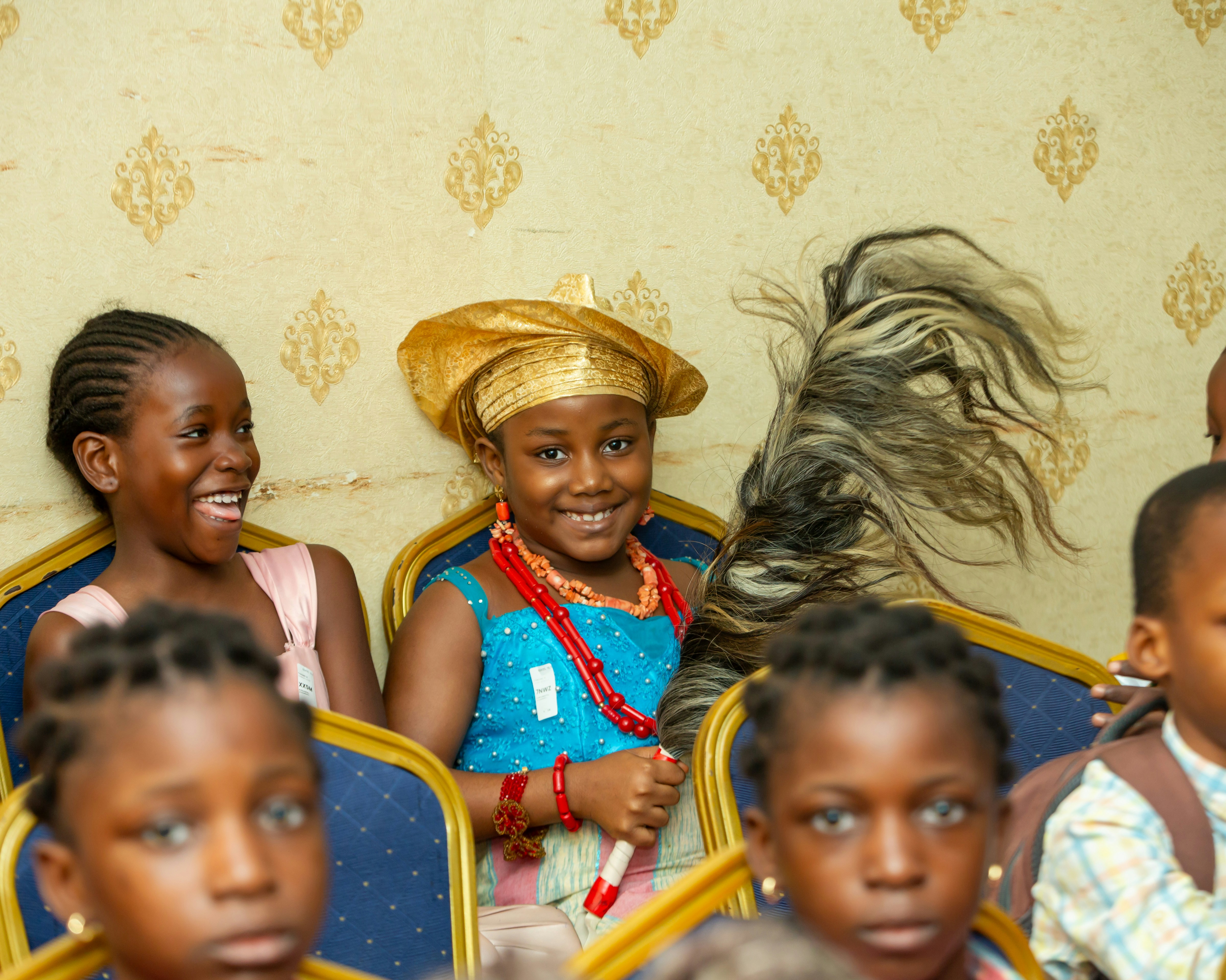 Two girls share smiles while dressed in traditional attire, surrounded by other children in a festive atmosphere.