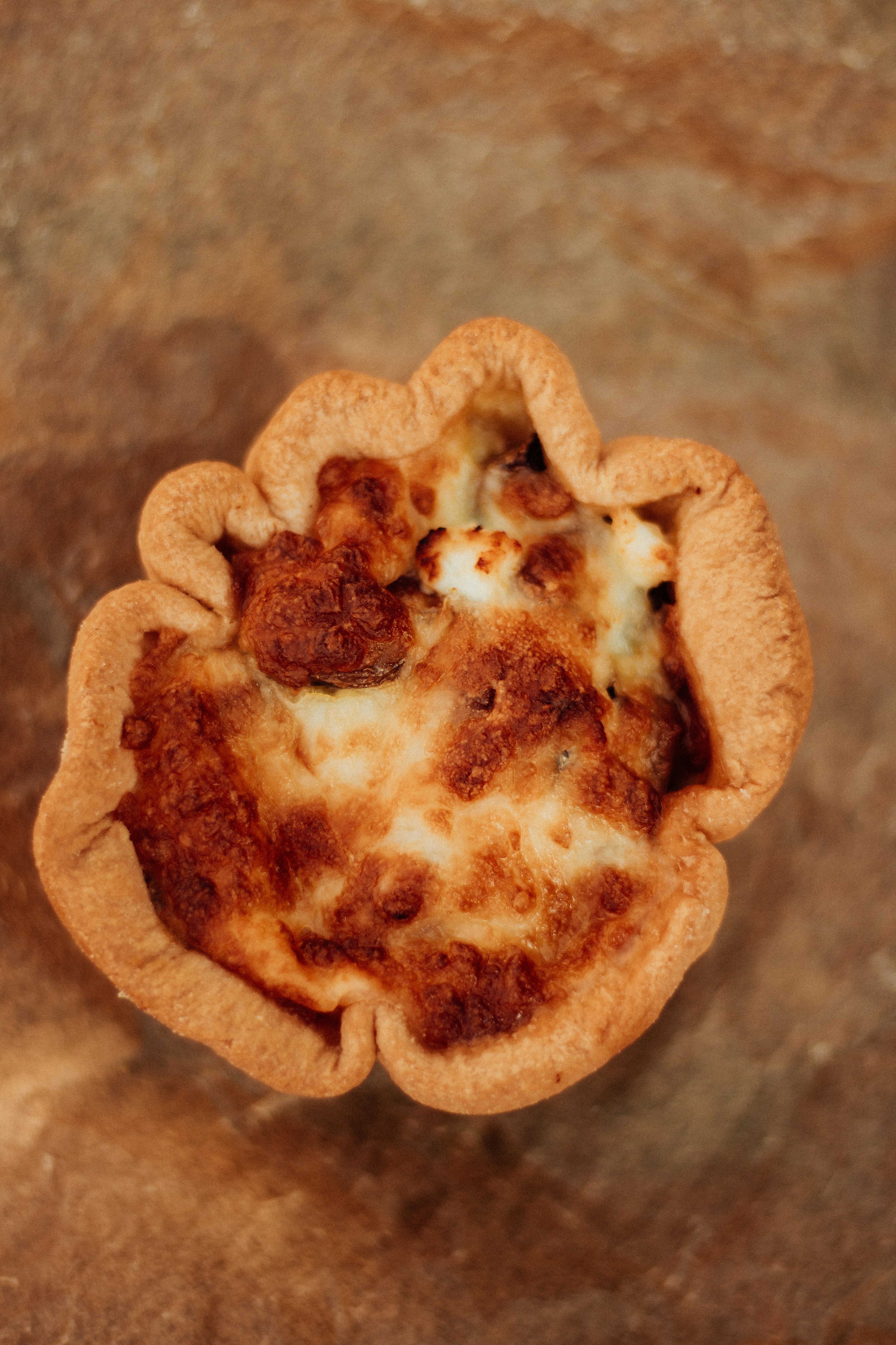 Golden-brown pastry filled with melted cheese and savory ingredients, showcasing a rustic presentation on a textured surface.