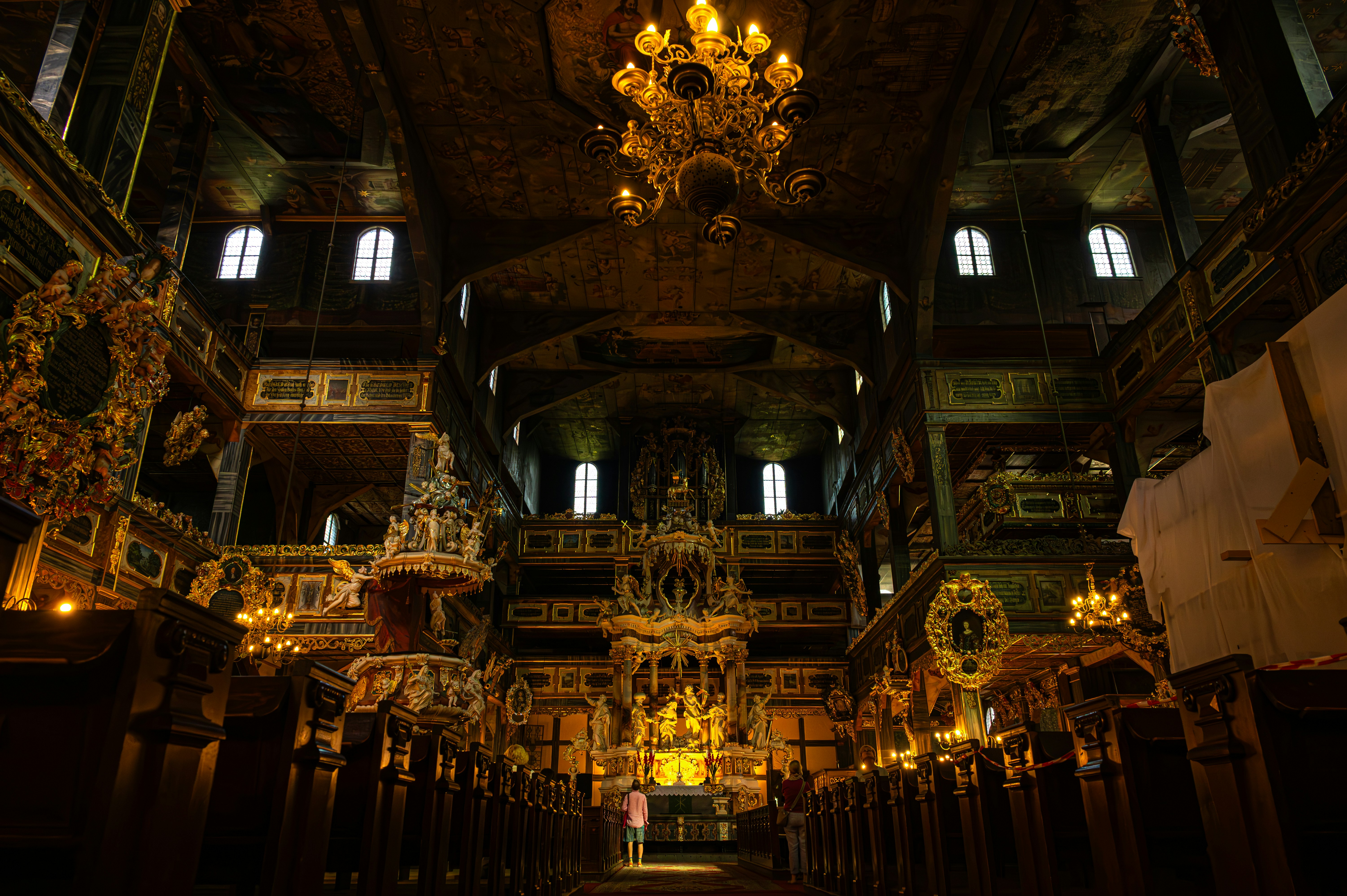 Intricate interior of a historic church featuring ornate decorations, a grand chandelier, and soft candlelight illuminating the pews.