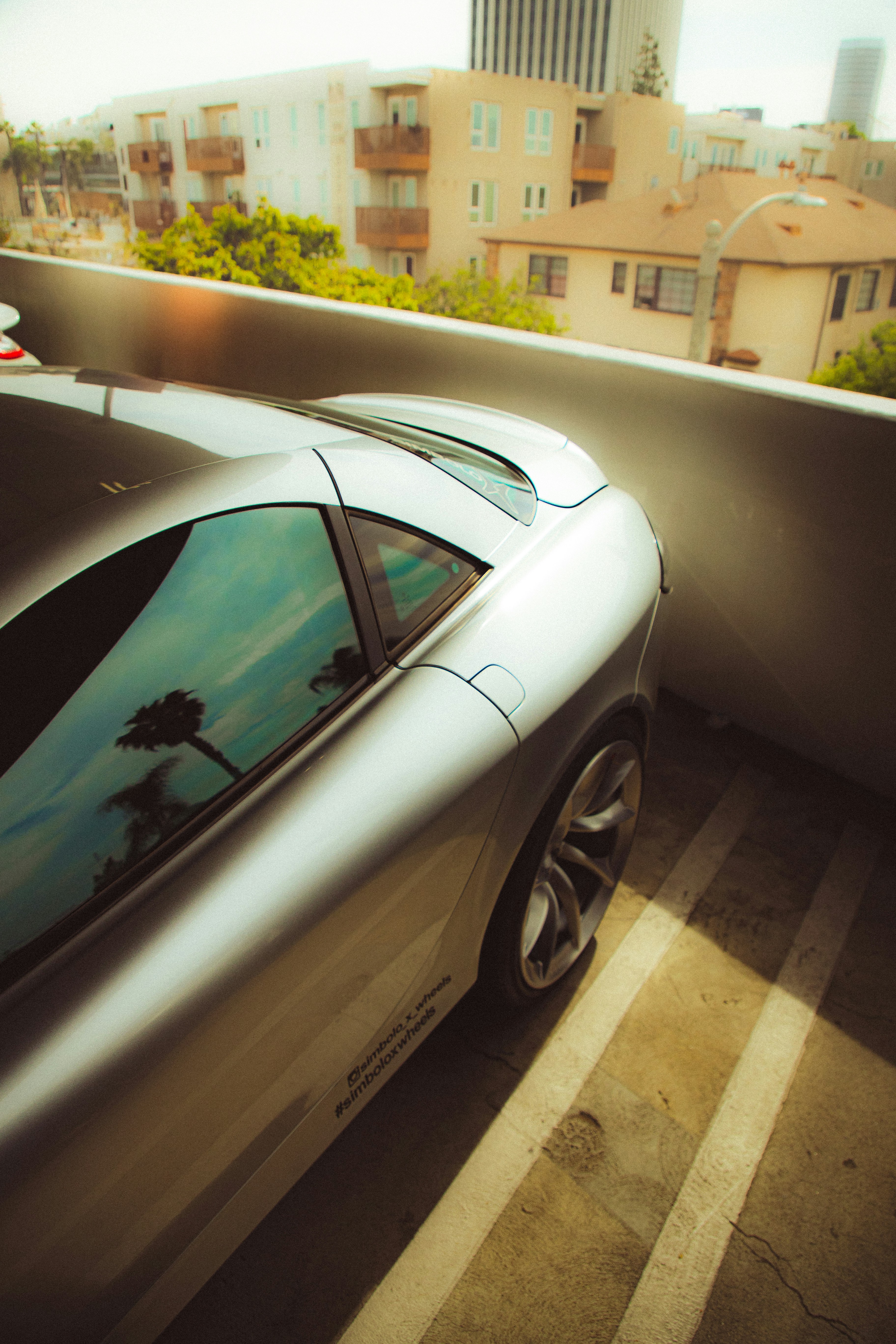 Rooftop Velocity: A Silver Sports Coupe Reflects Palm Shadows and City Lines