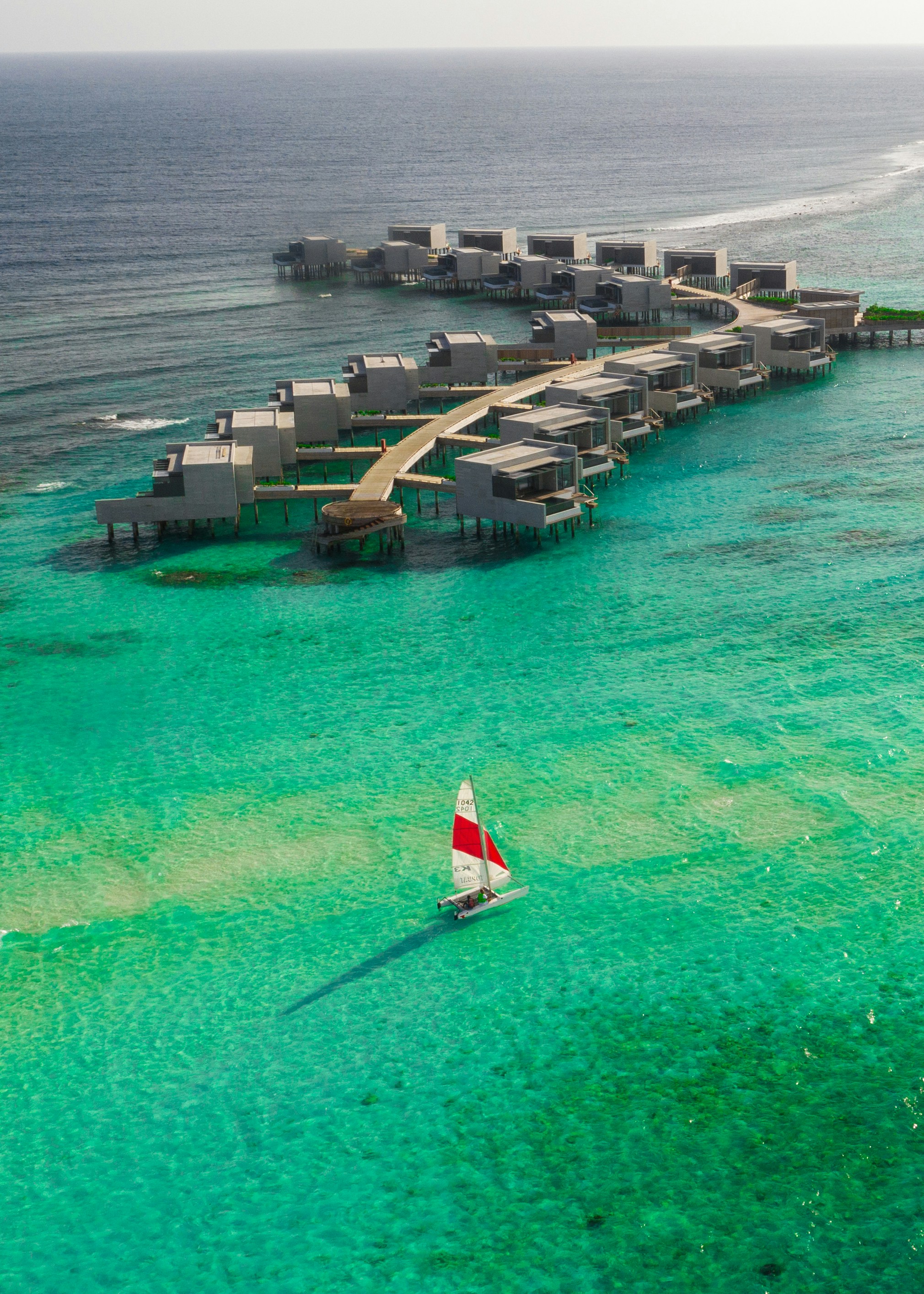 Sailboat gliding through turquoise waters near modern overwater bungalows, showcasing a tranquil coastal escape.