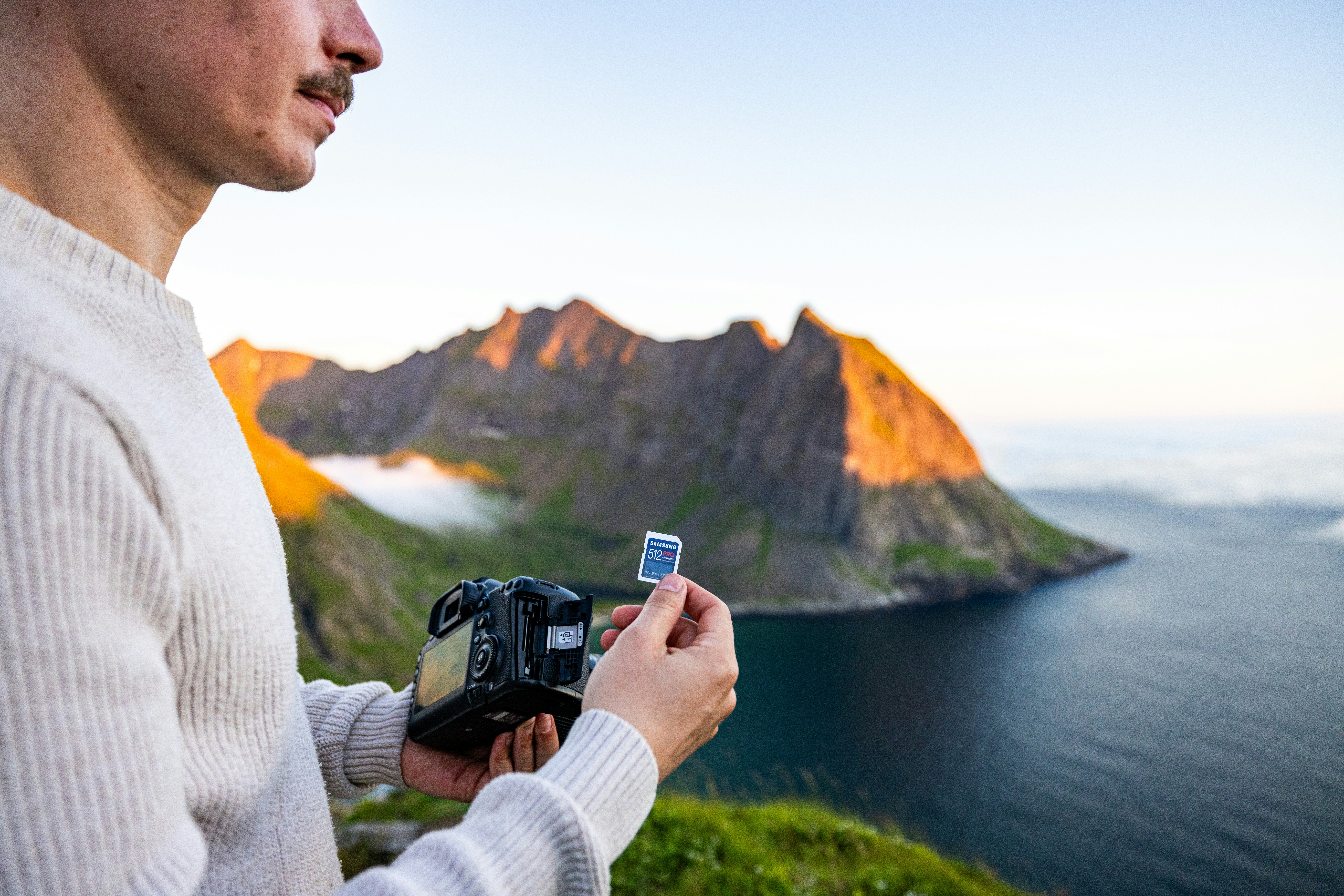 Man holding sd card with camera and mountain landscape.