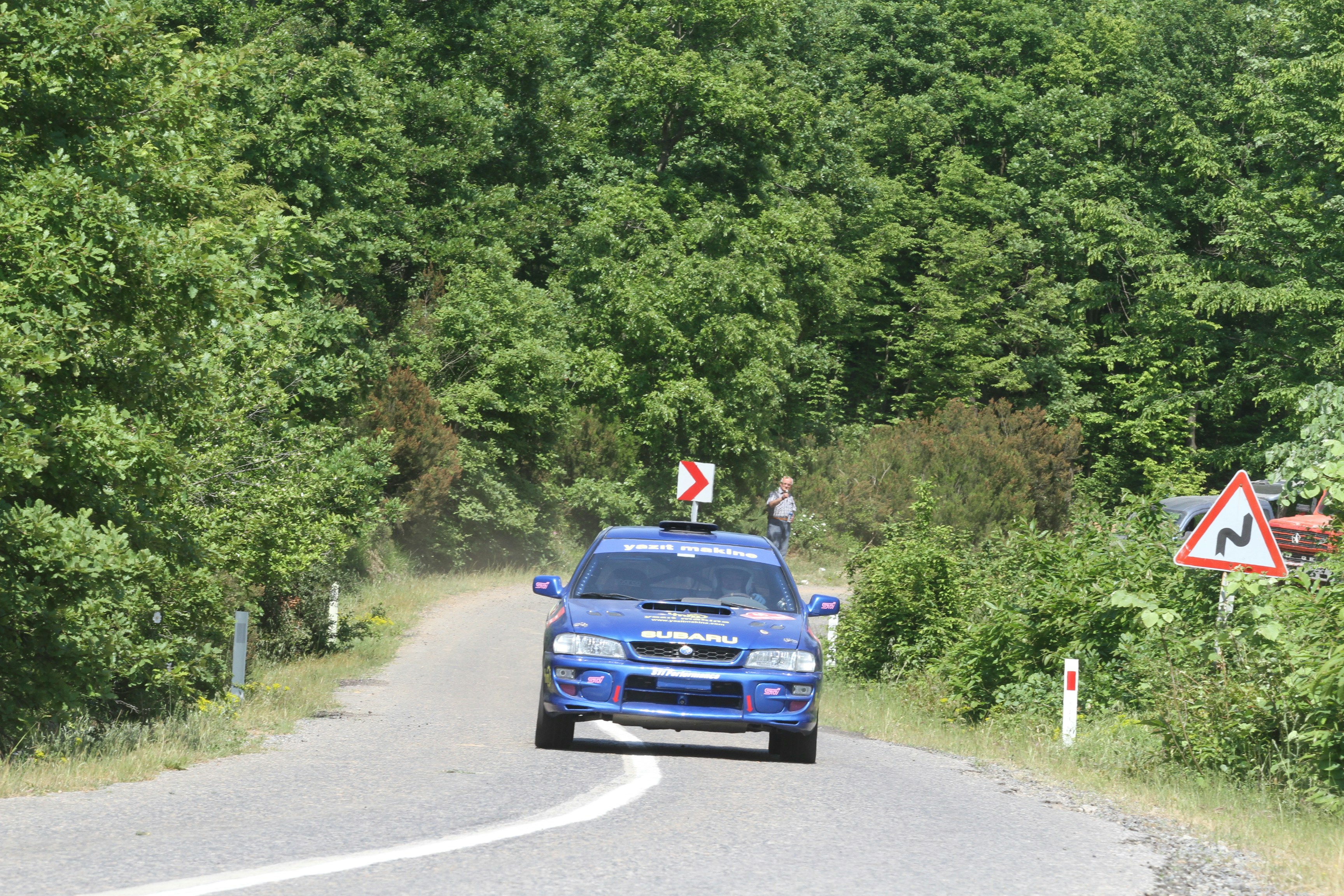 Blue car driving on a winding road through trees