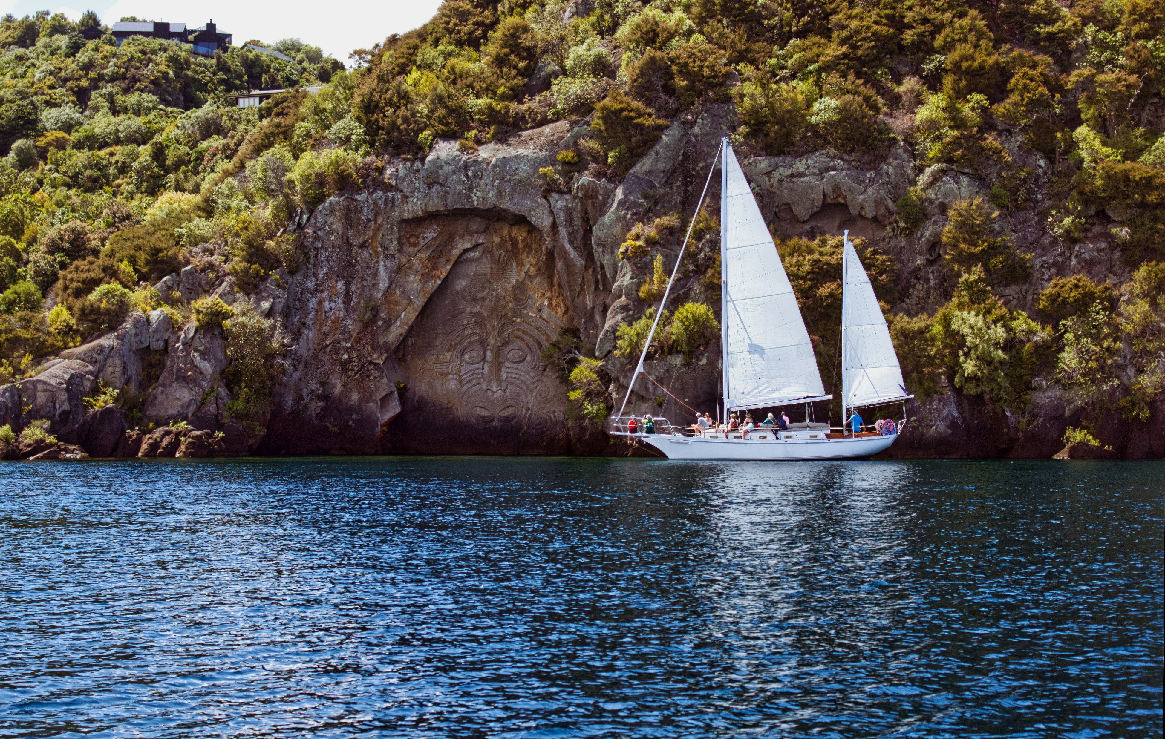 Boat to the rock carving | Sailboat glides past a rocky, forested coastline.