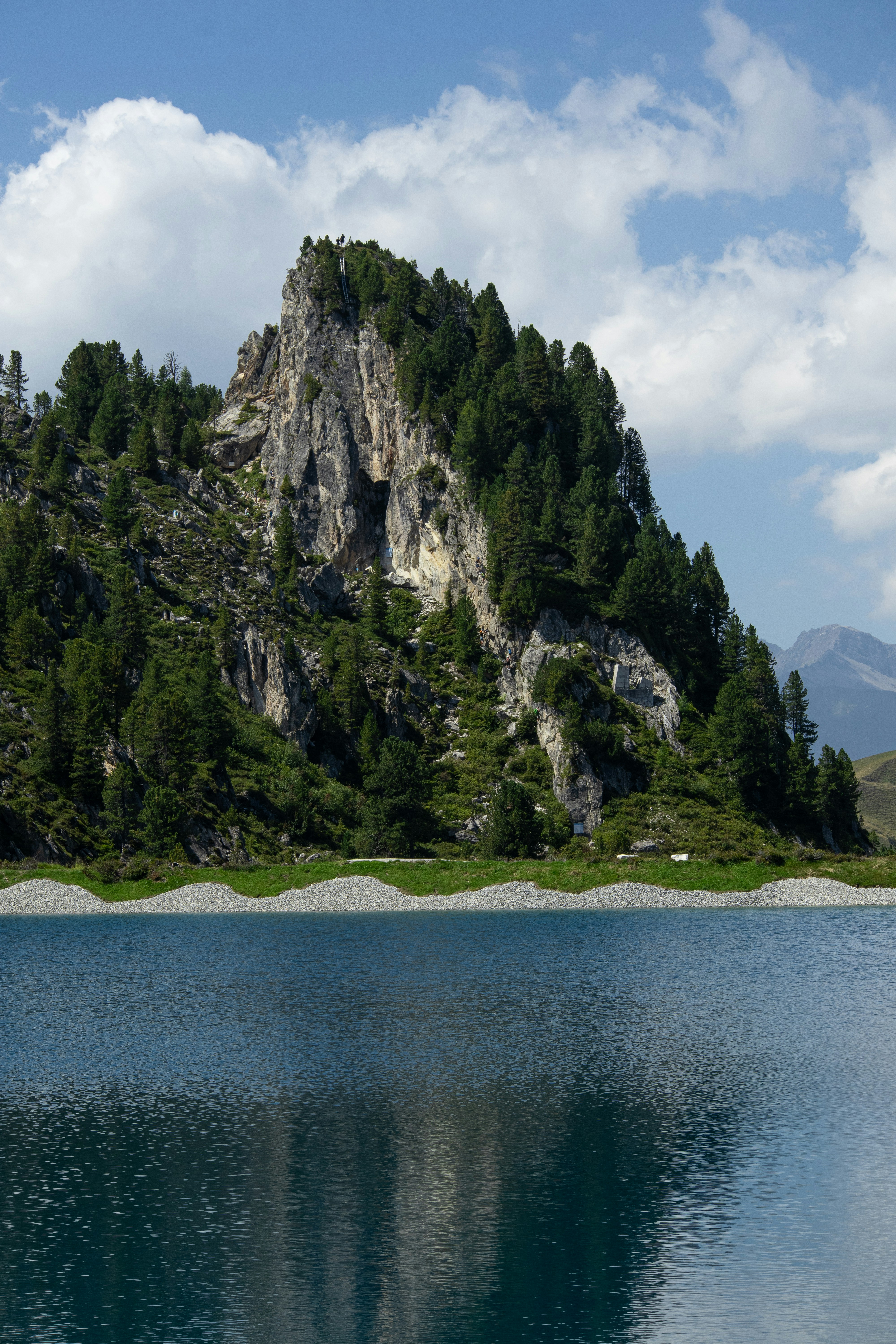 Rocky mountain peak covered in green trees above lake.