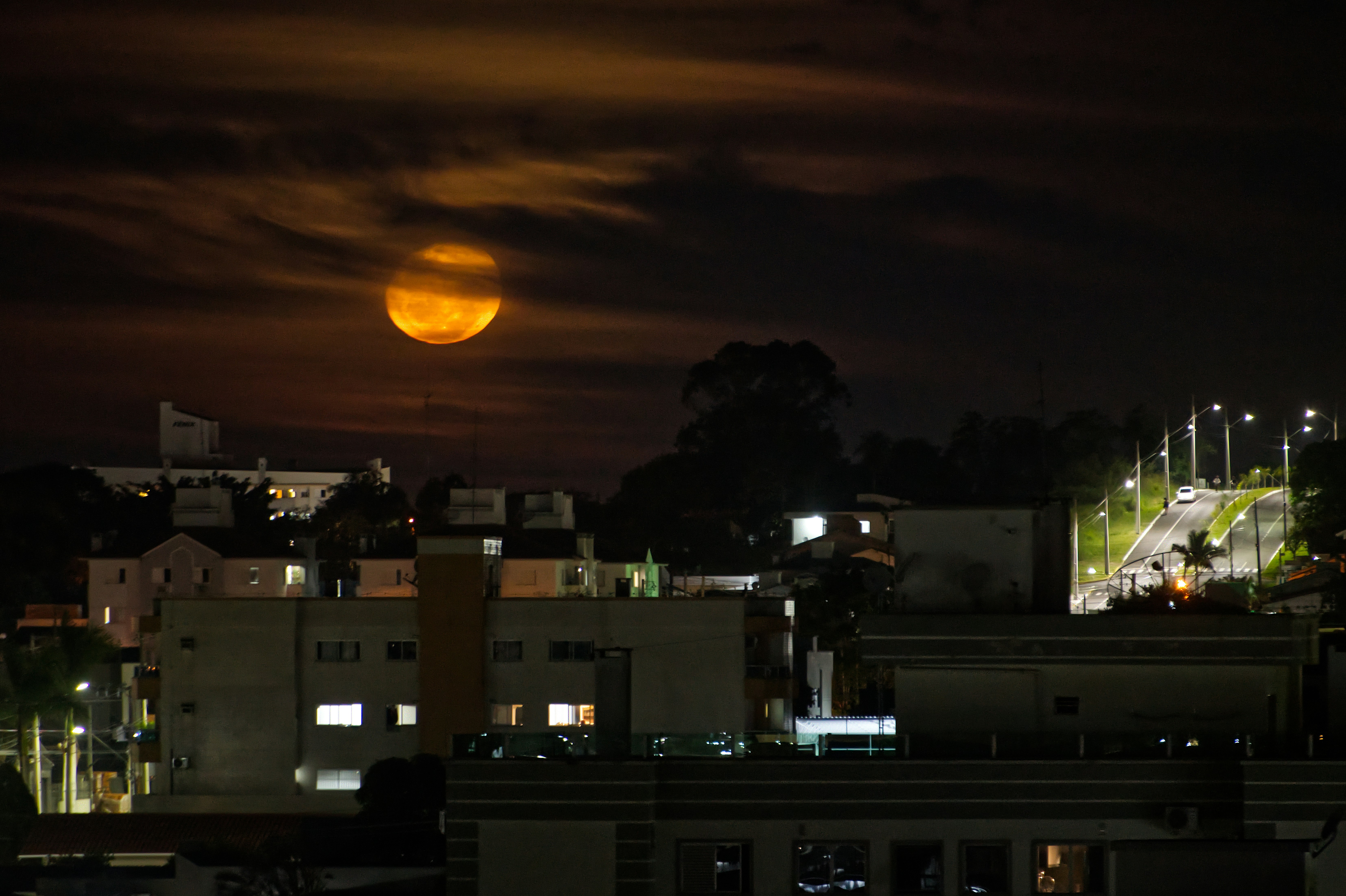 Full moon obscured by clouds over city buildings.