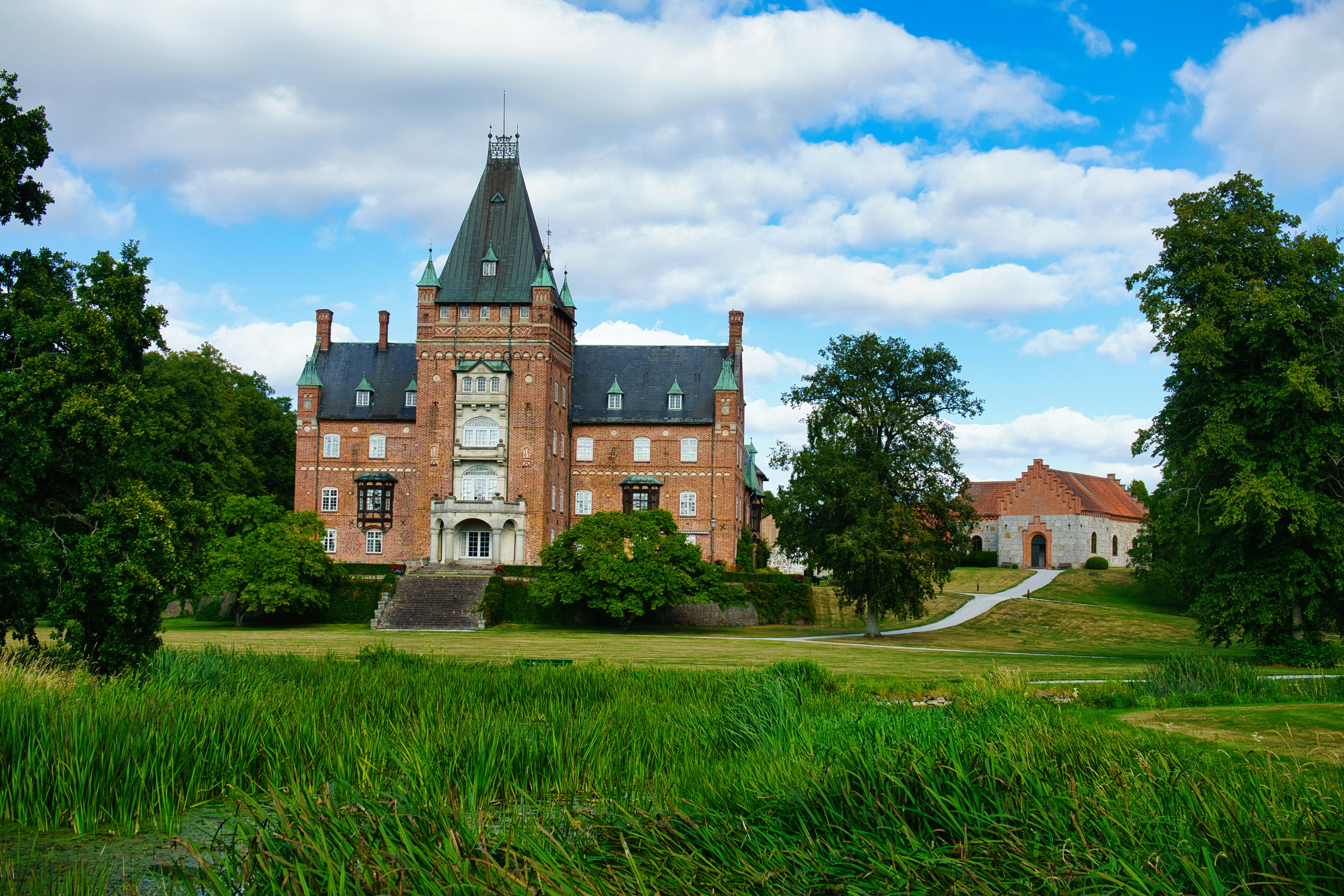 Trollenäs Castle | Historic brick castle with tall tower surrounded by greenery.