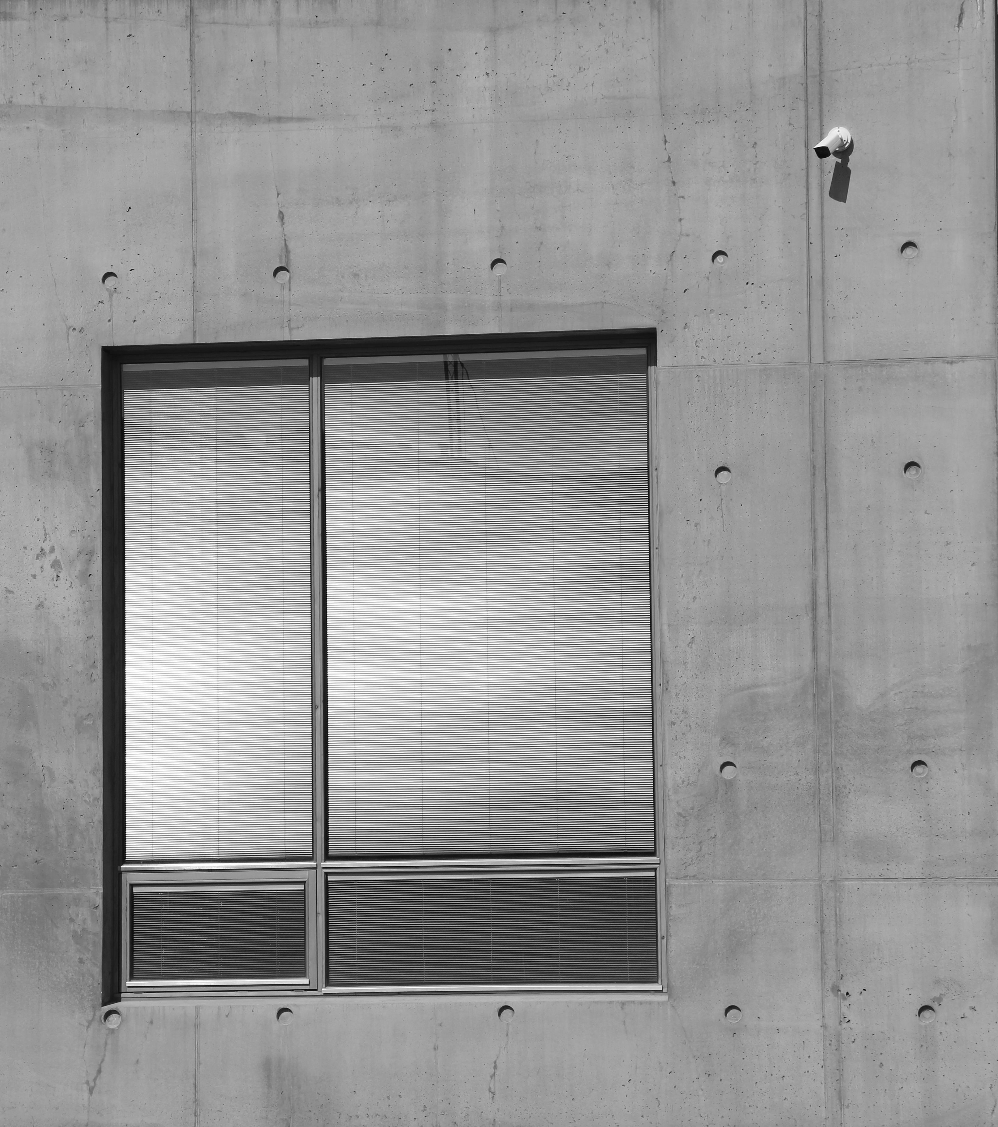 Modern concrete building with a large window and security camera.