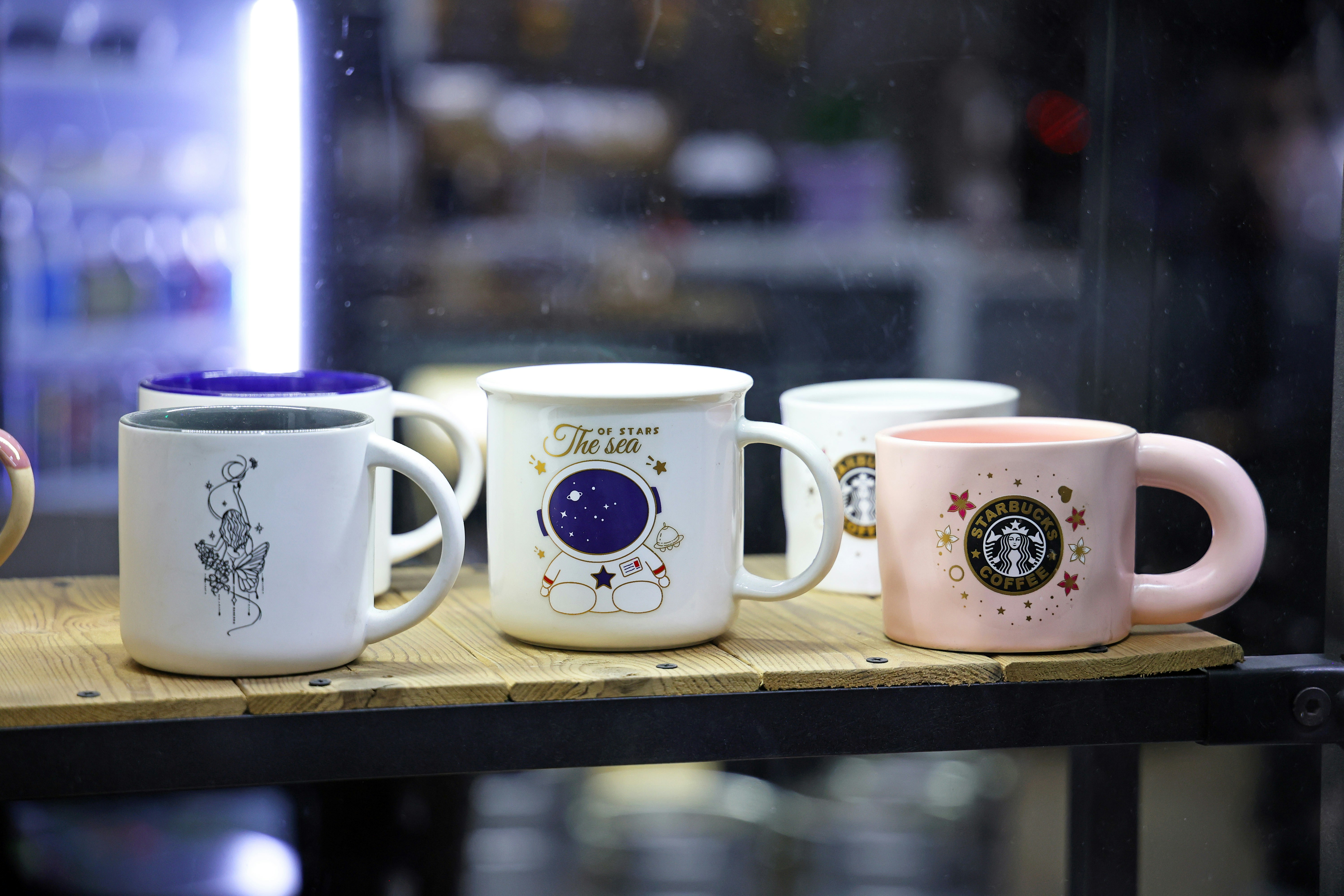 A collection of uniquely designed mugs displayed on a wooden shelf, showcasing playful illustrations and vibrant colors.