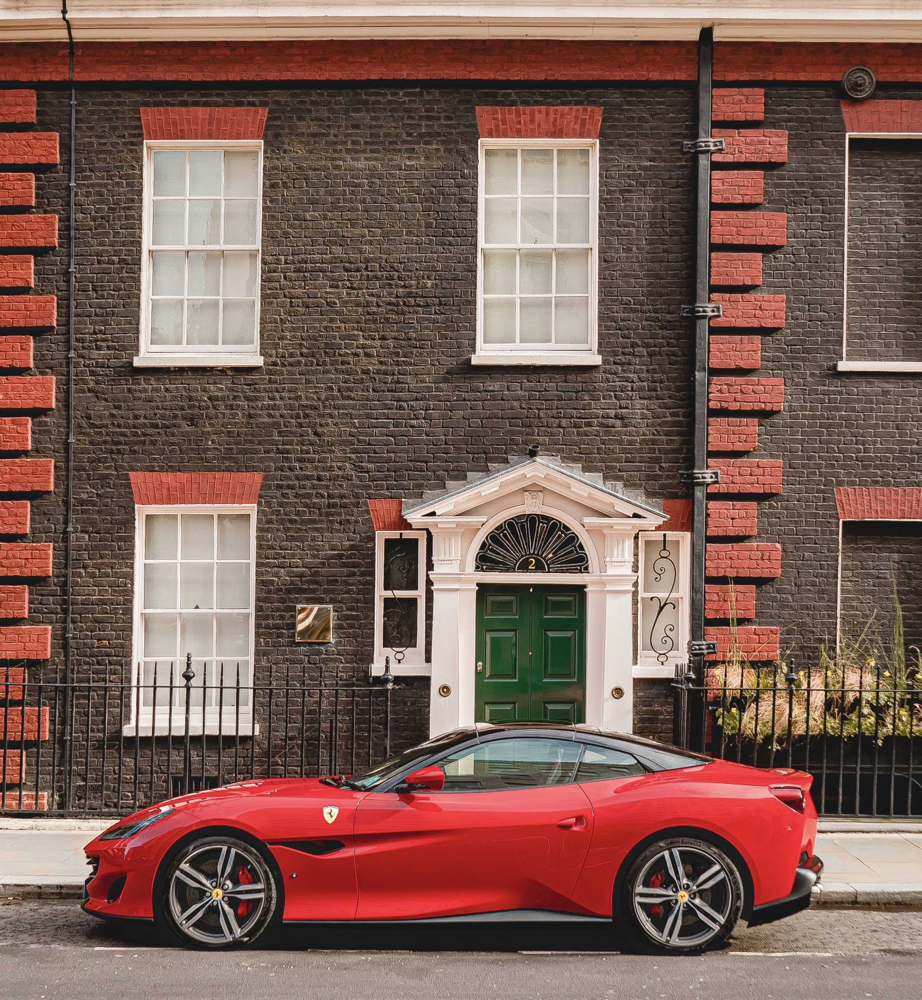A red Ferrari parked in front of classic architecture – where timeless design meets pure performance. | Red sports car parked in front of a brick building.