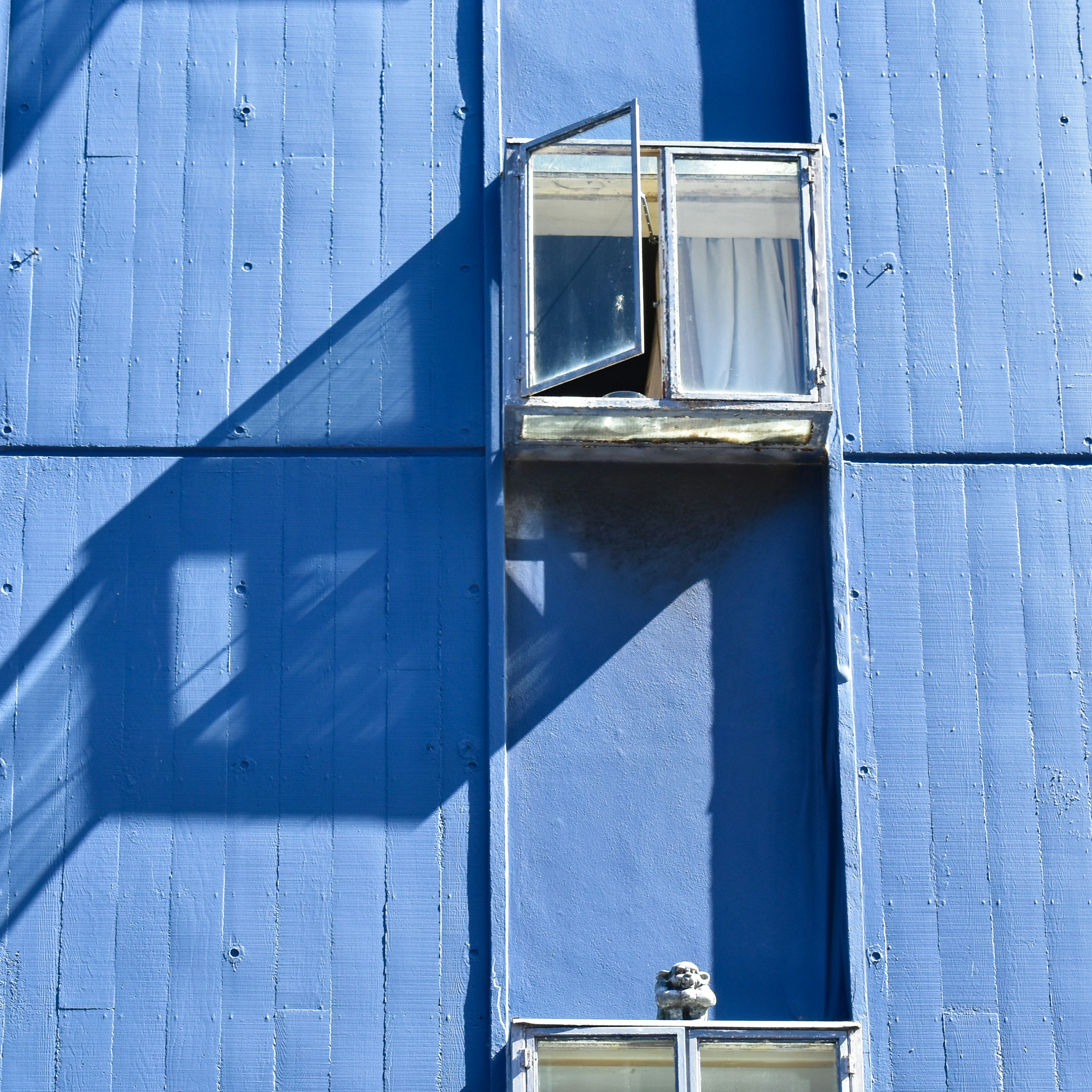 An open window and its shadow on a house with a blue facade | Blue building facade with open window and shadow