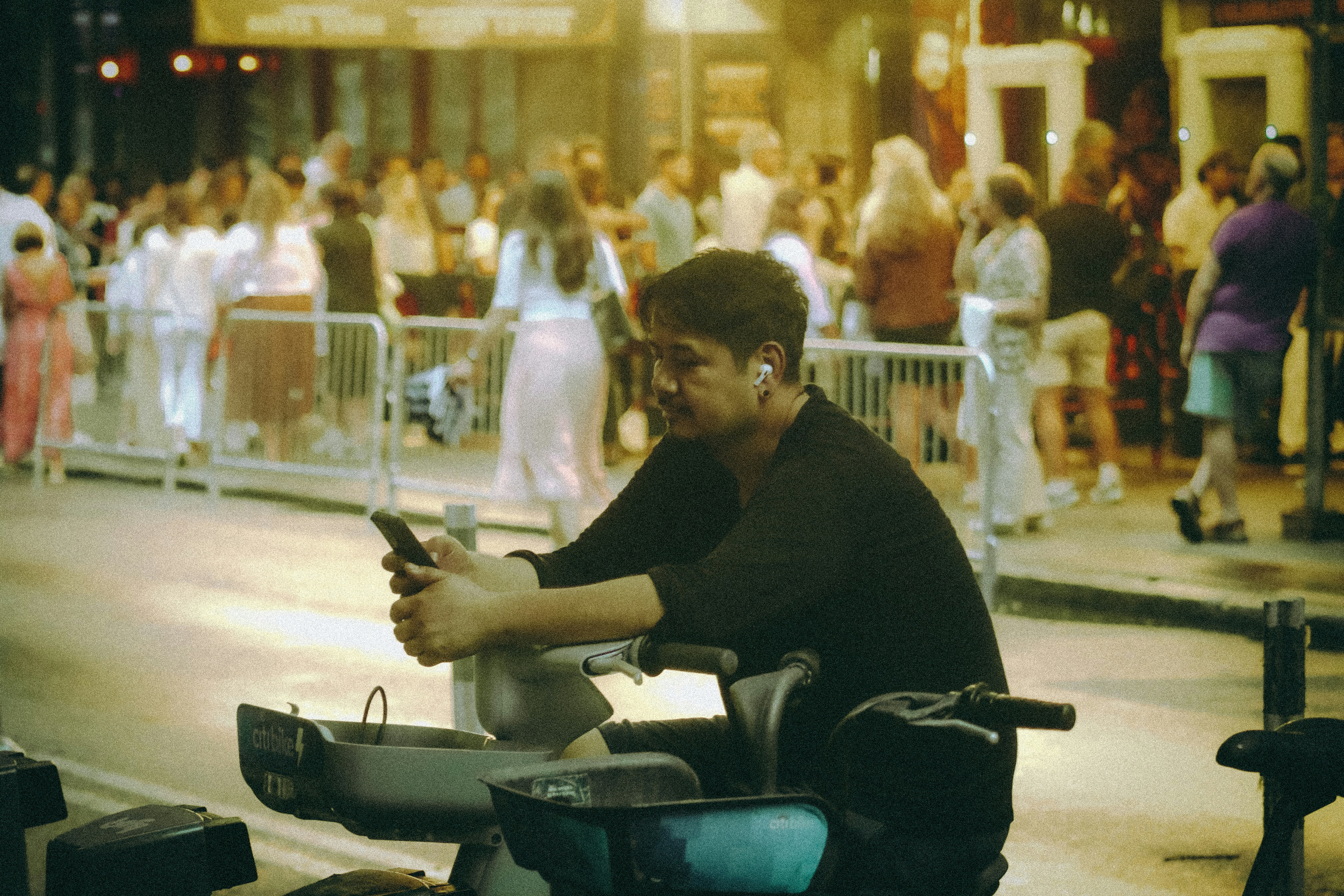 Man on scooter looking at phone with crowd behind