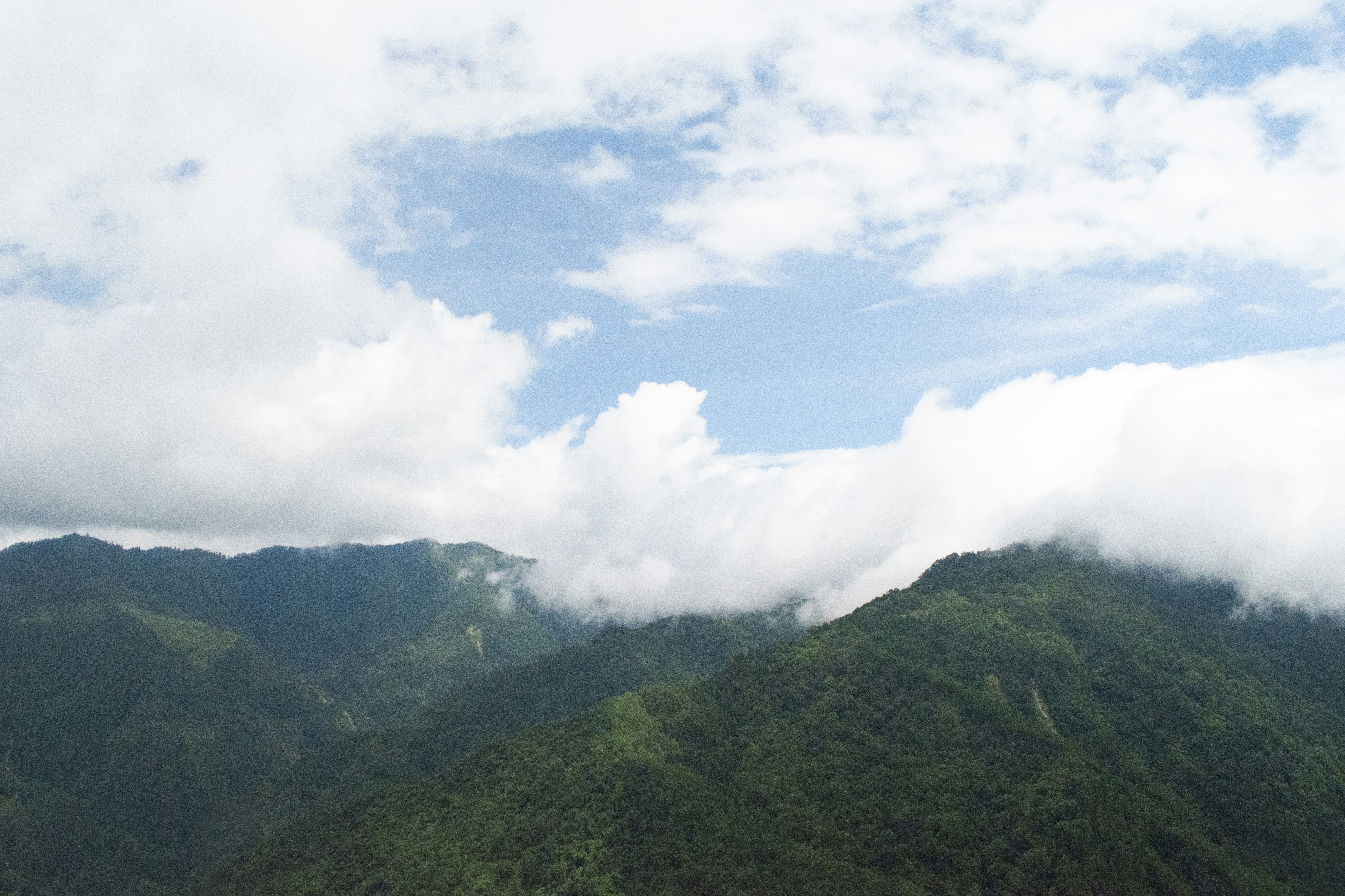 Lush green mountains under a partly cloudy sky, with mist gently hovering over the peaks. The scene captures the serene beauty of nature.