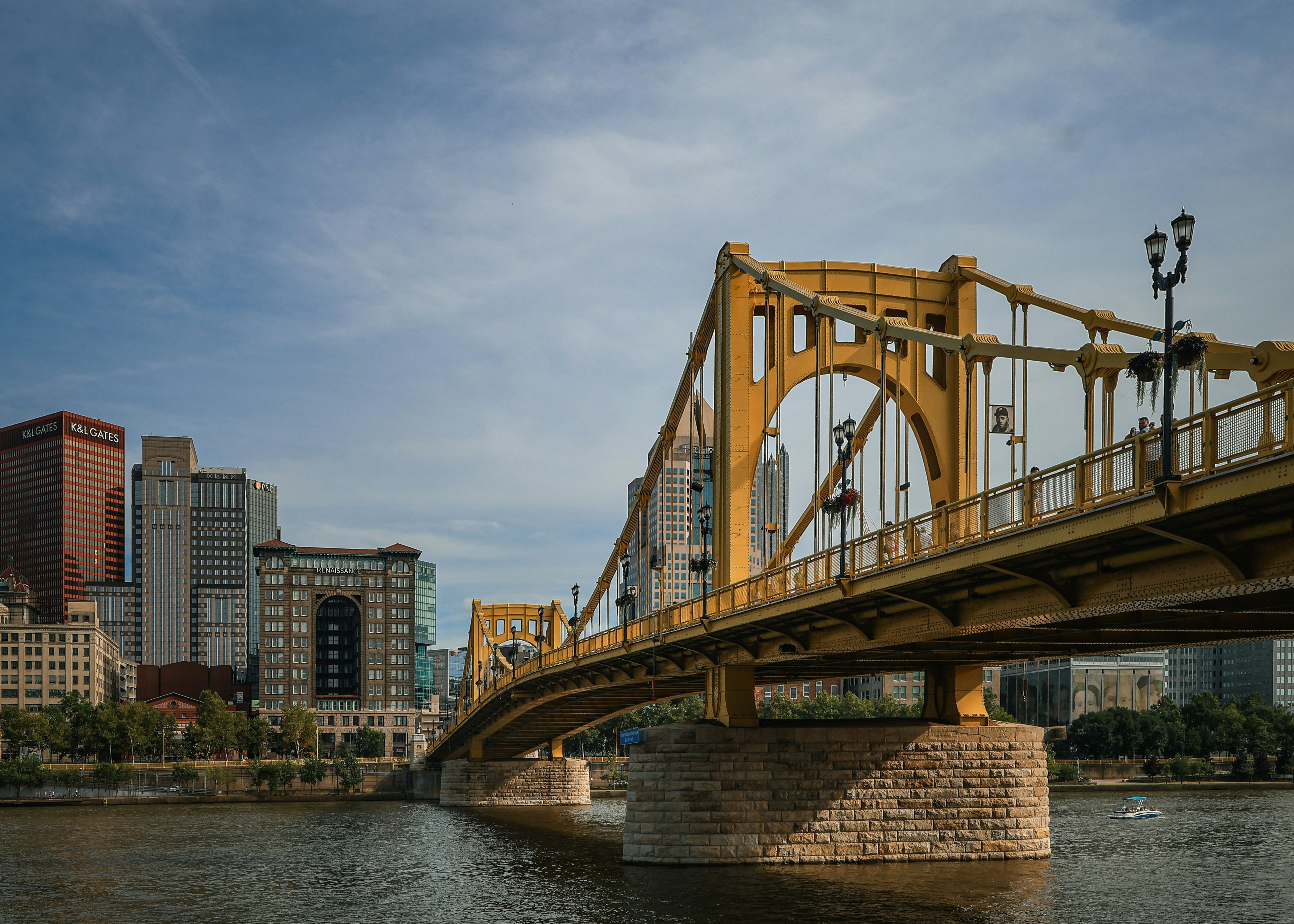 The Roberto Clemente Bridge in Pittsburgh PA, with the skyline in the background. | Yellow suspension bridge over a river with city skyline.