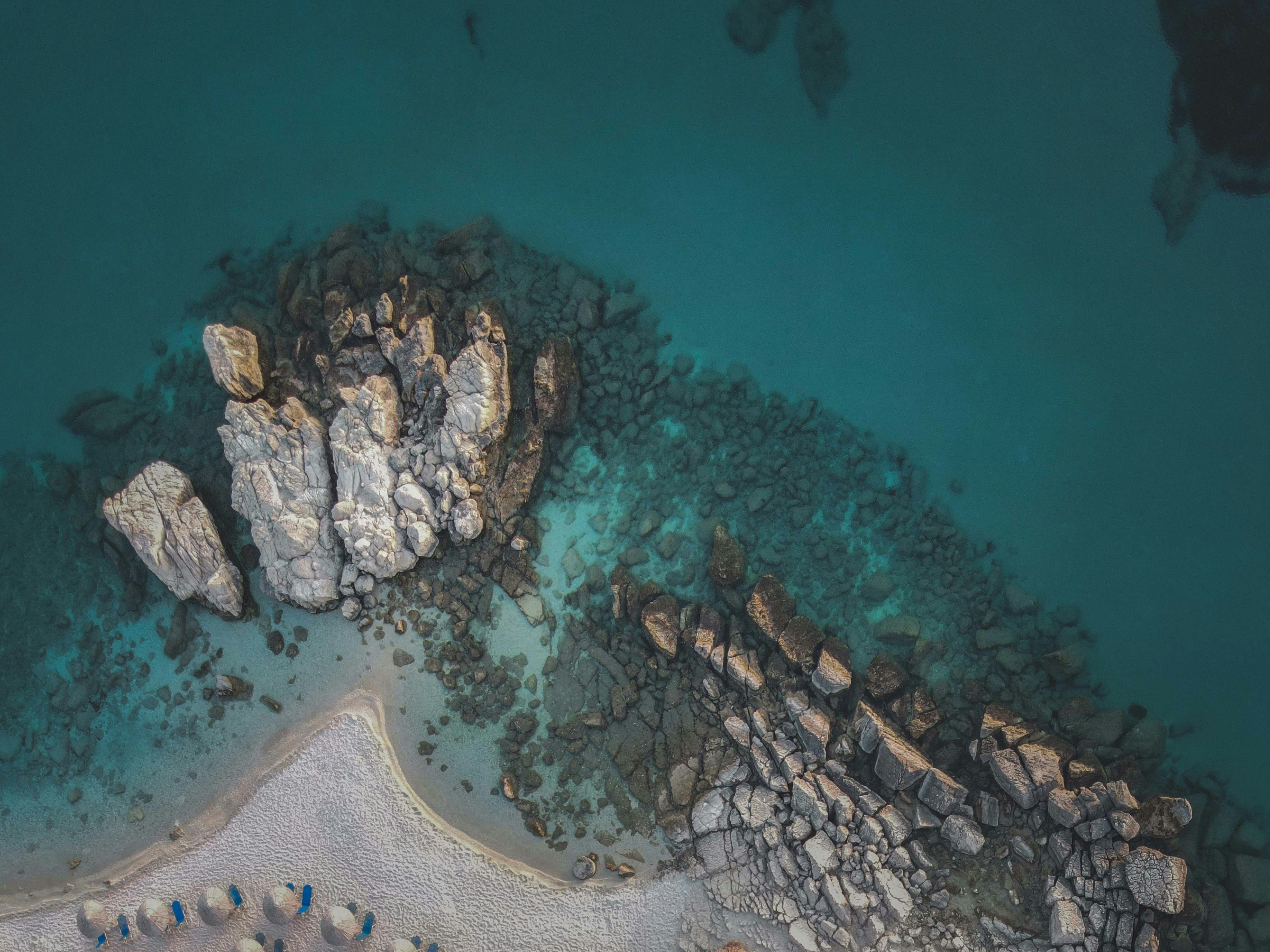 Rocky outcrop emerging from crystal-clear waters, framed by a sandy beach and scattered beach umbrellas. The tranquil scene invites exploration and relaxation.